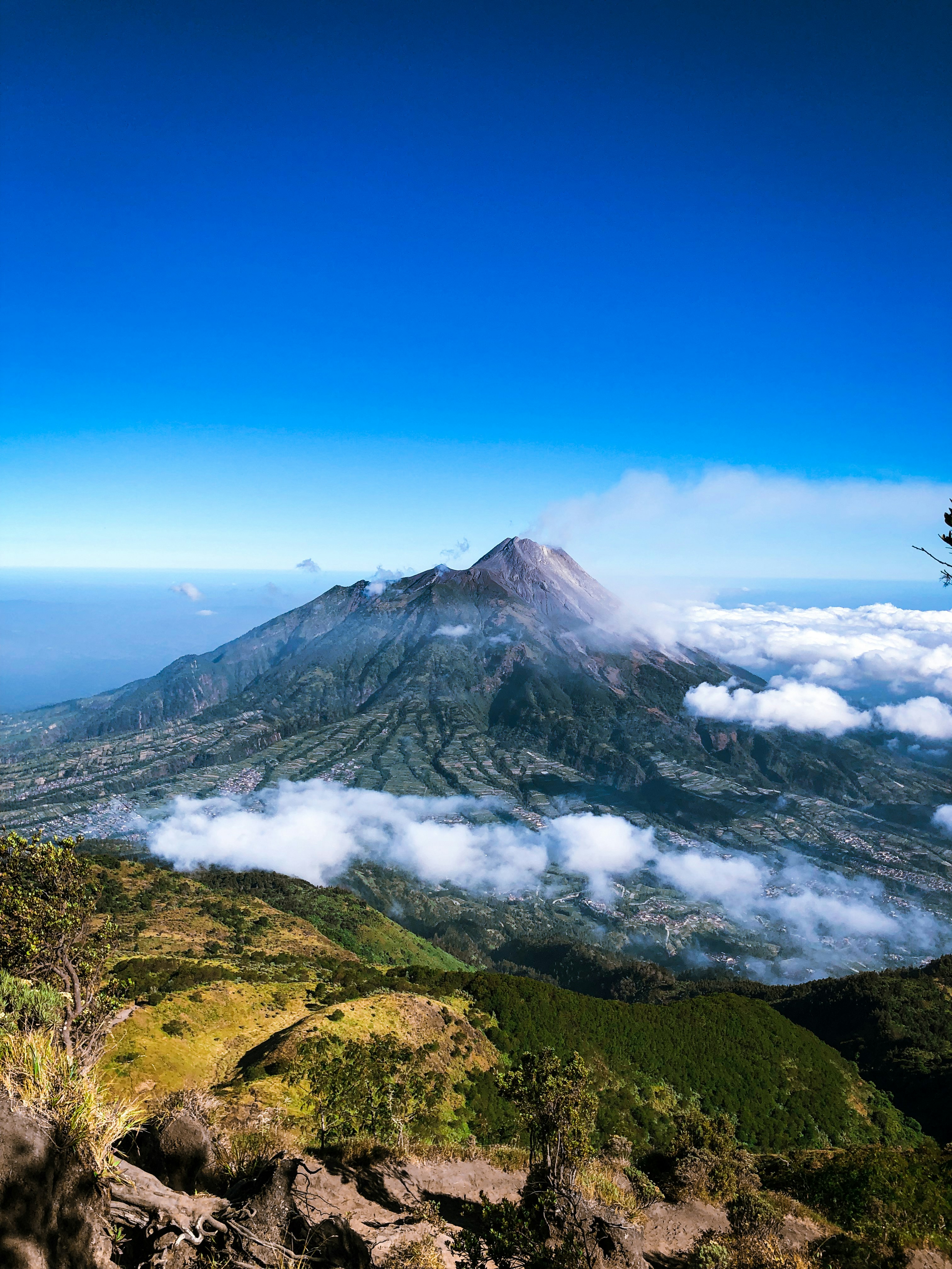 Volcano rising majestically above a patchwork of green valleys and clouds, showcasing the beauty of nature's contrasts.