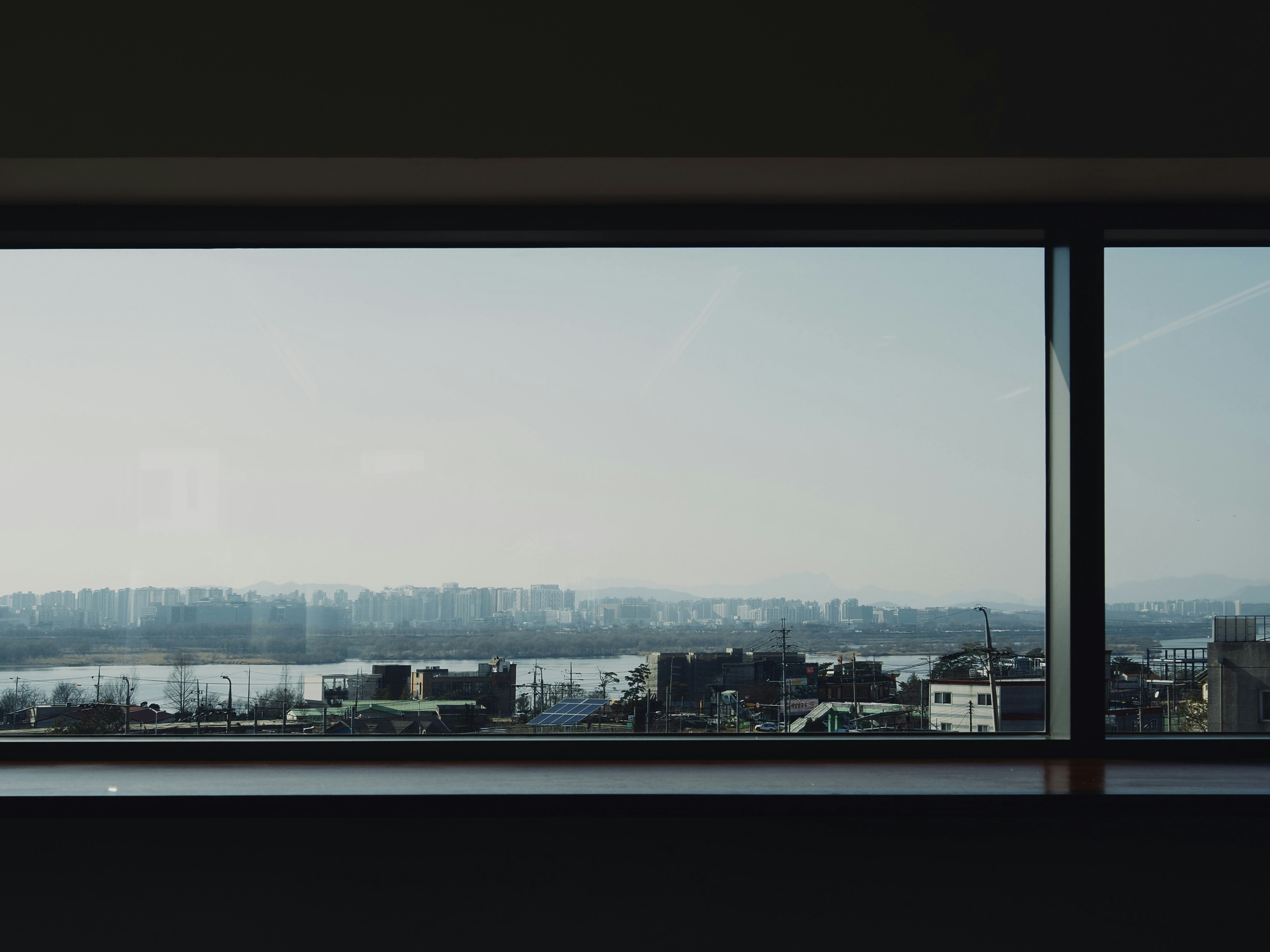 A serene view of a cityscape framed by a large window, showcasing distant buildings and a river under a hazy sky.