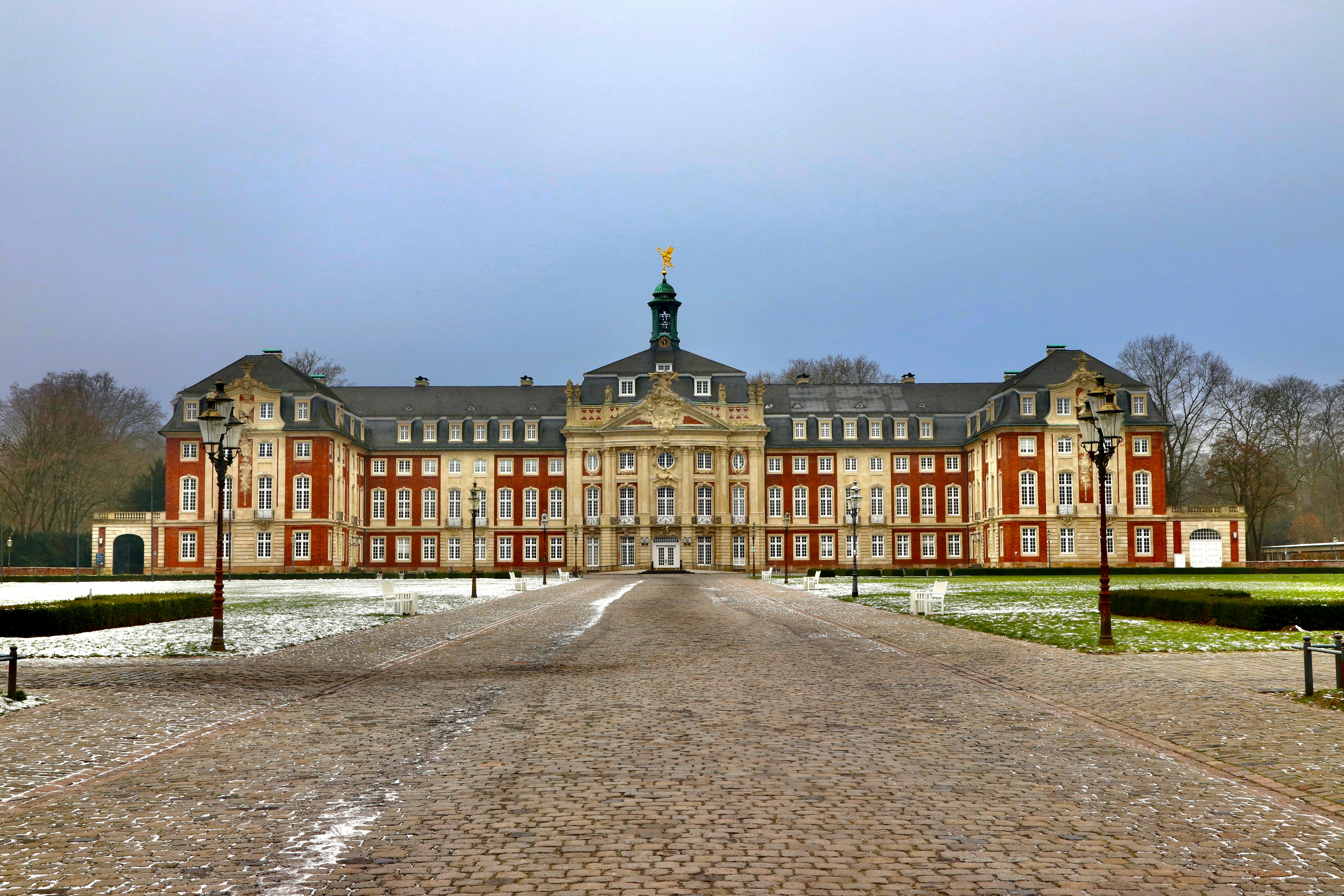Grand historic building with a clock tower, framed by a symmetrical facade and surrounded by a wintry landscape.