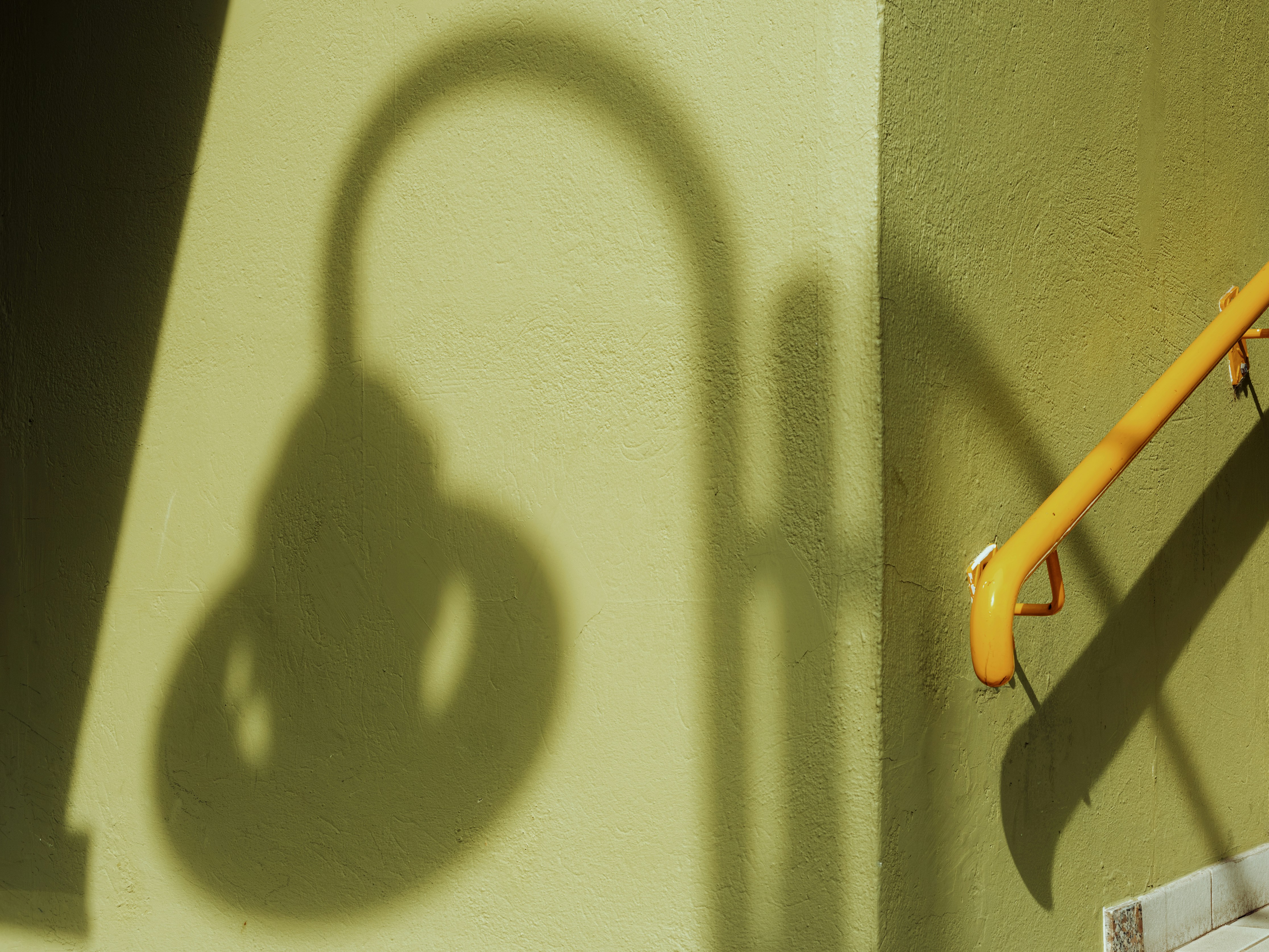 a shadow of a yellow handle on a green wall