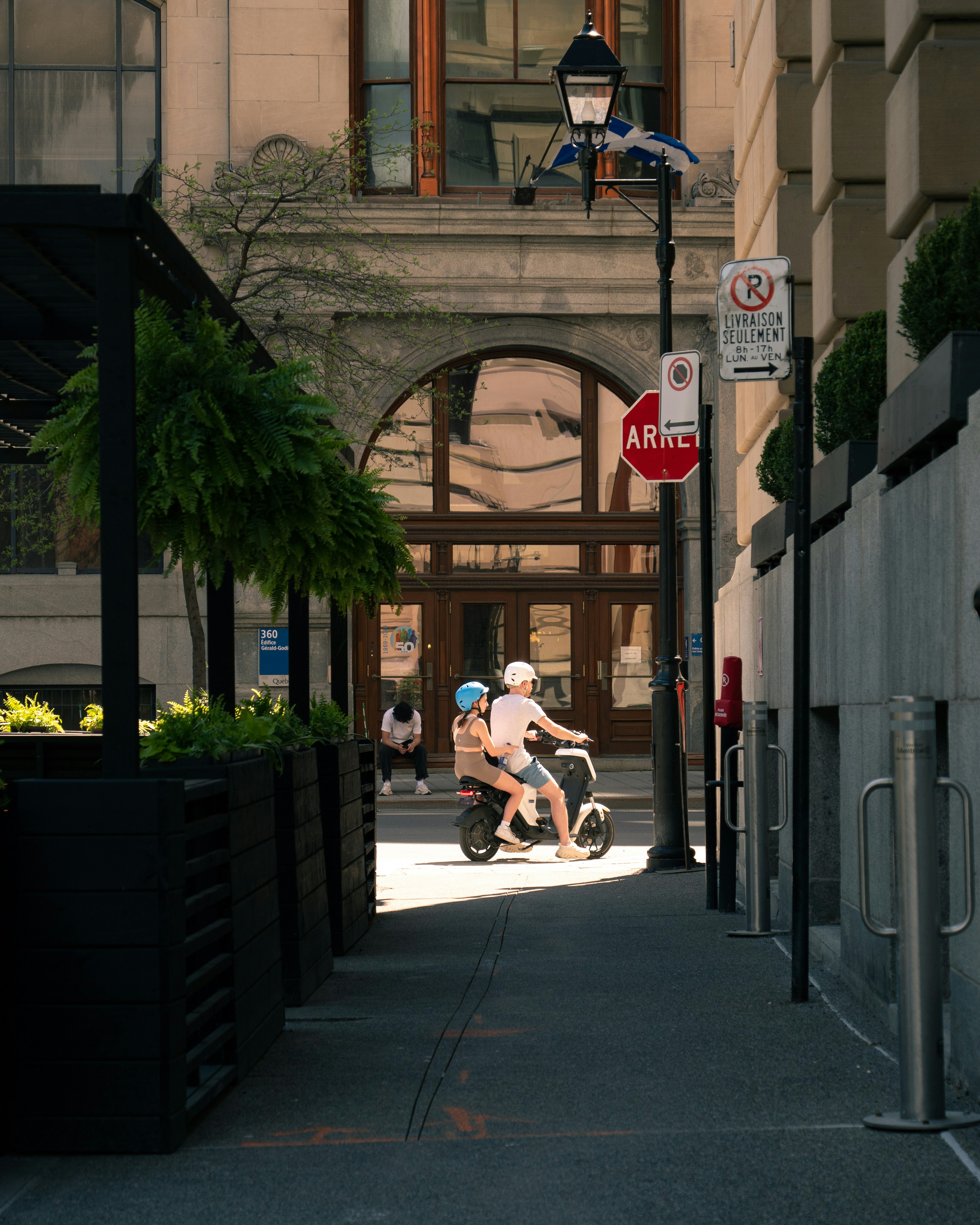 Sunlit Archway: Scooter Duo Navigates a Quiet City Corridor