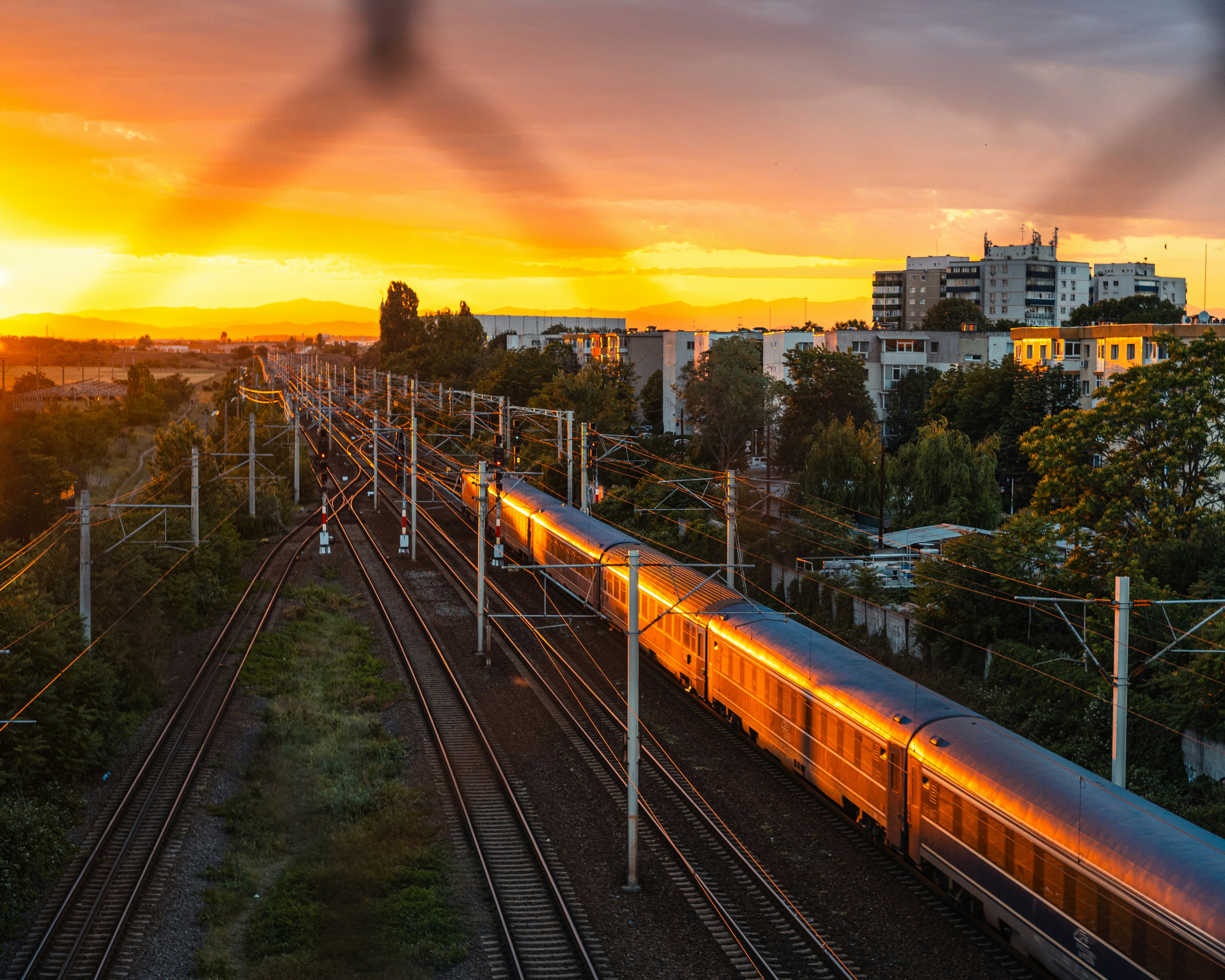 Sunset Rails: An Orange Train Traverses a Golden Suburban Horizon