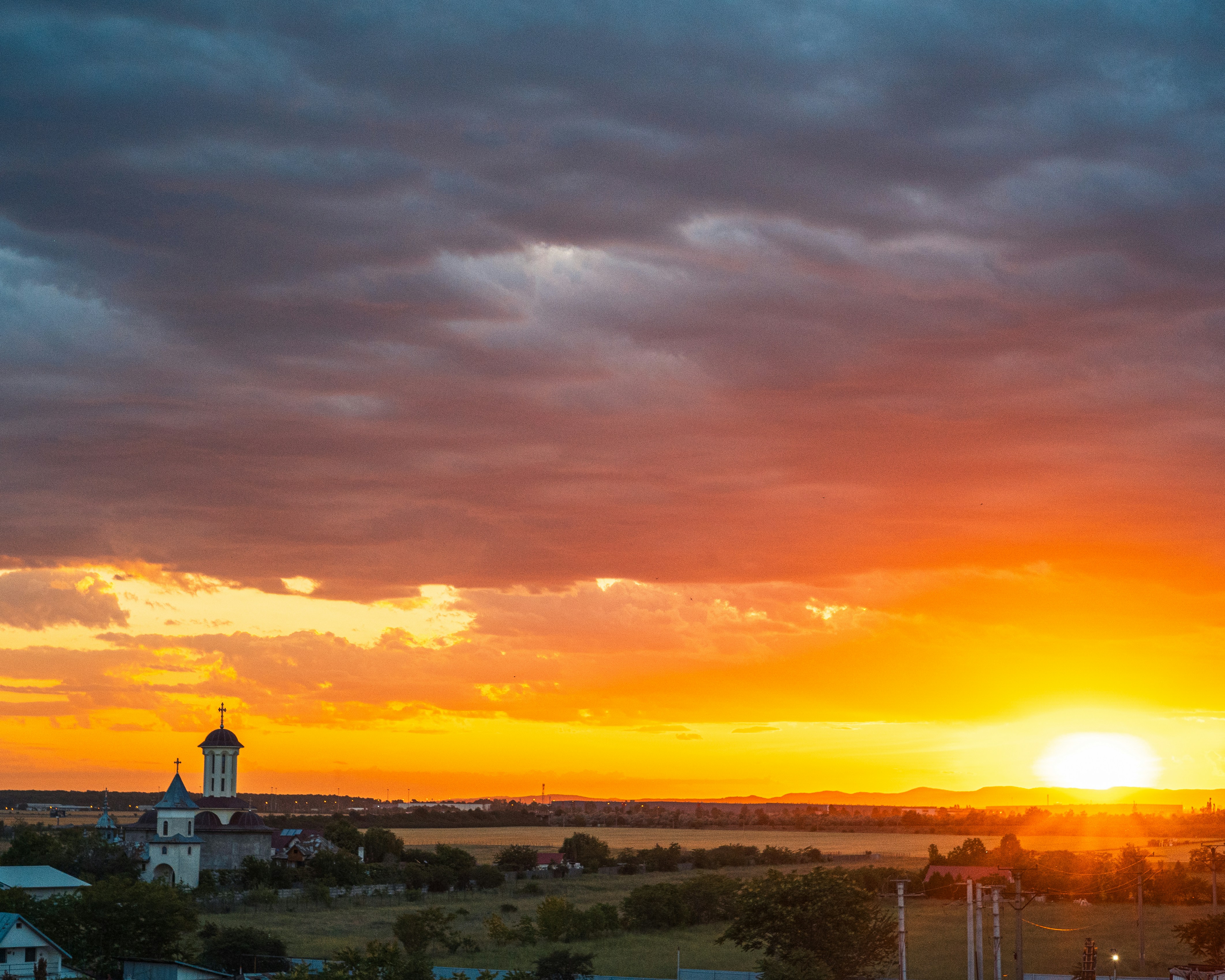 Ember Horizon: Sunset over a quiet town with a church spire and distant water gleaming