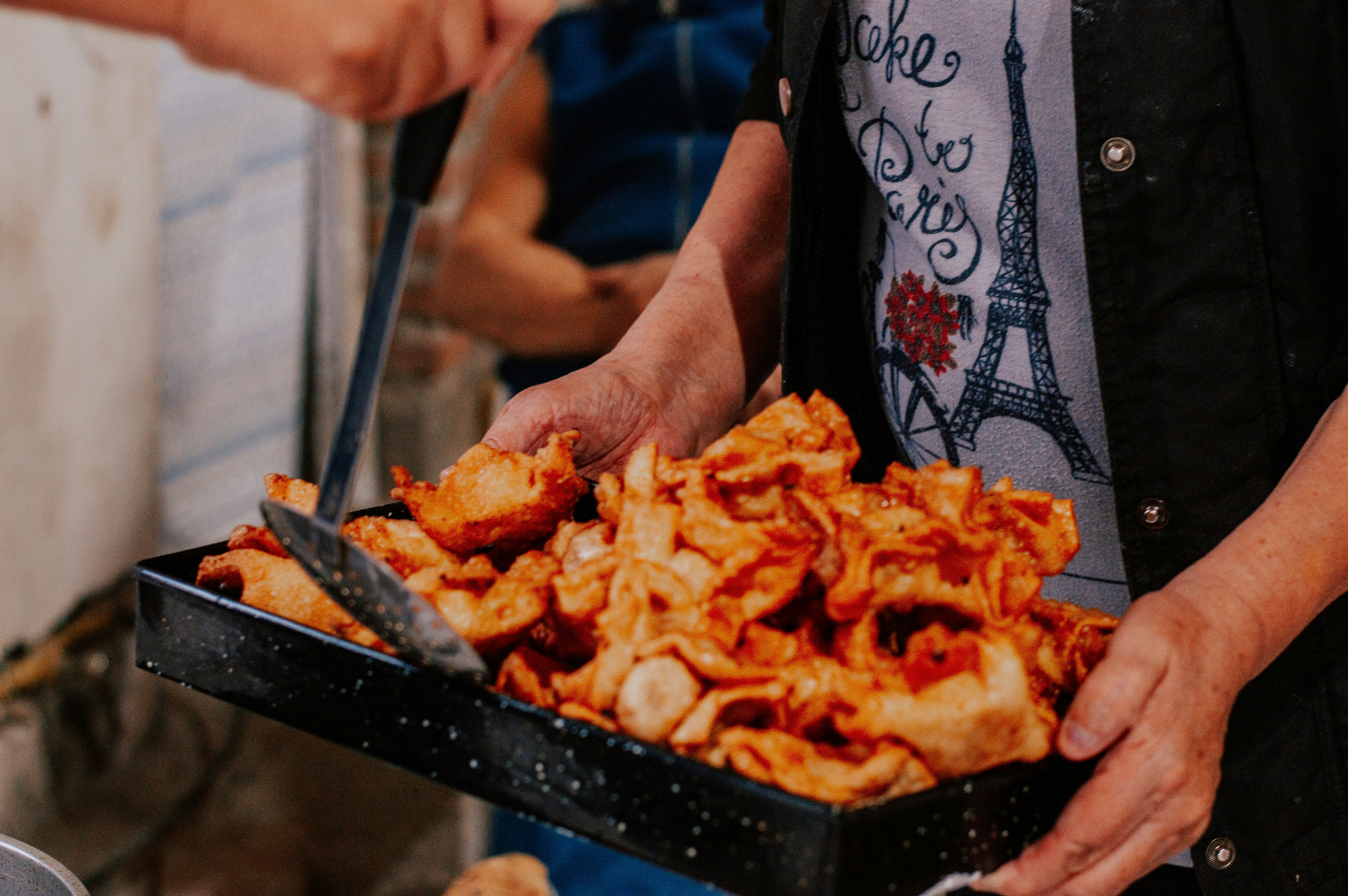 Person holding a tray of pastries with an Eiffel Tower design on their shirt.