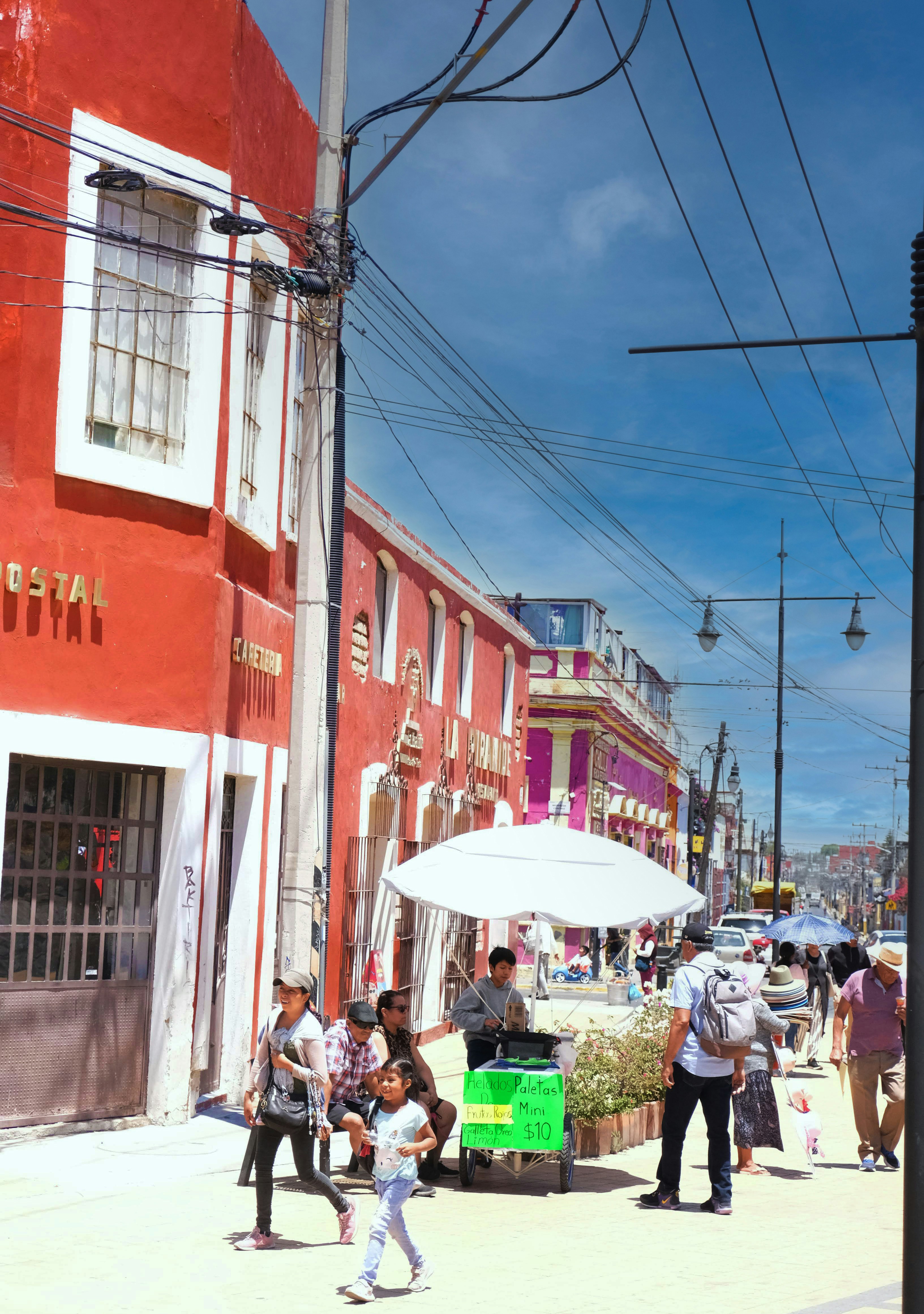 Crimson Facades and a White Umbrella: A Sunlit Street Market in Motion
