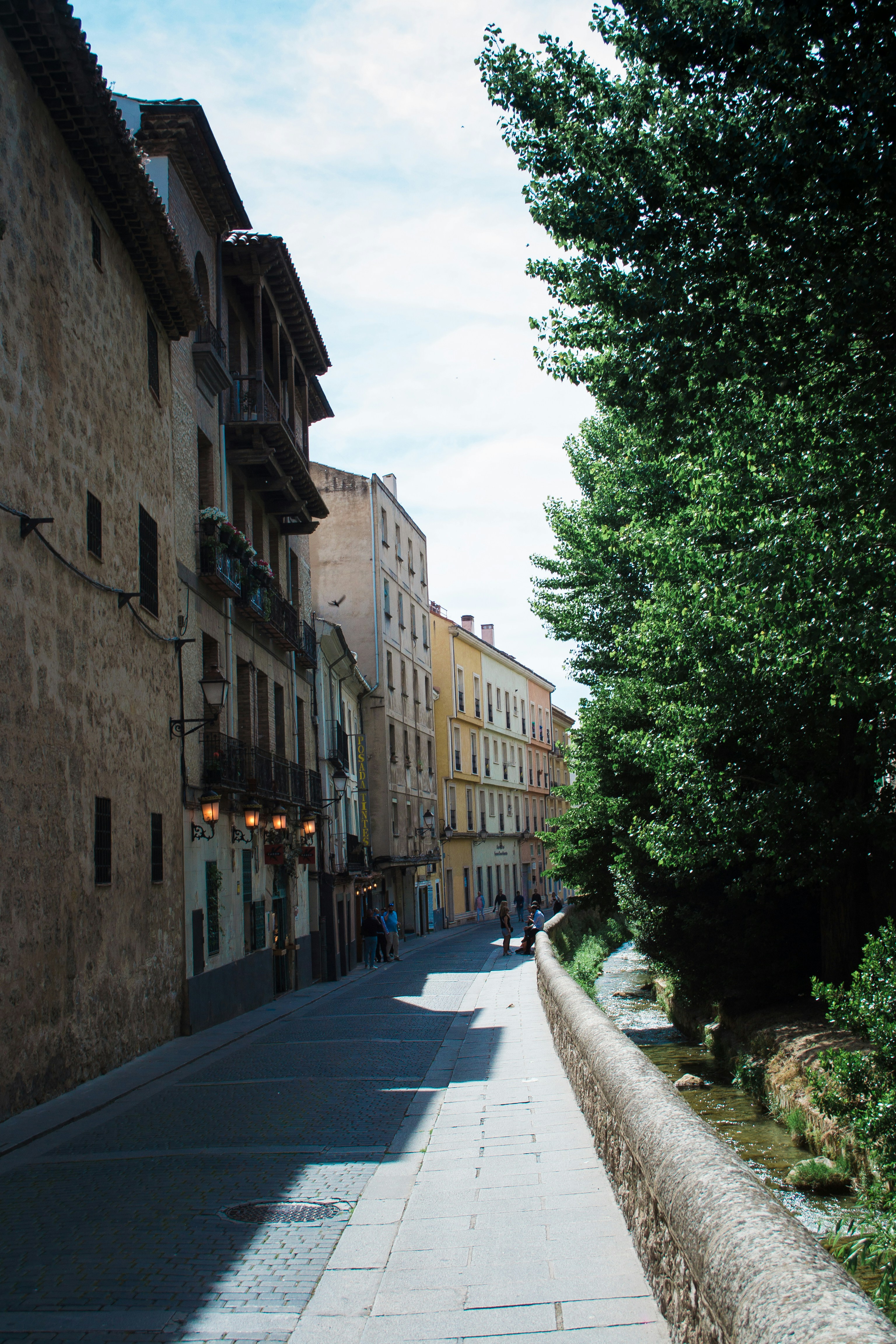 Sunlit Calle: A Quiet Path Between Old Walls and River
