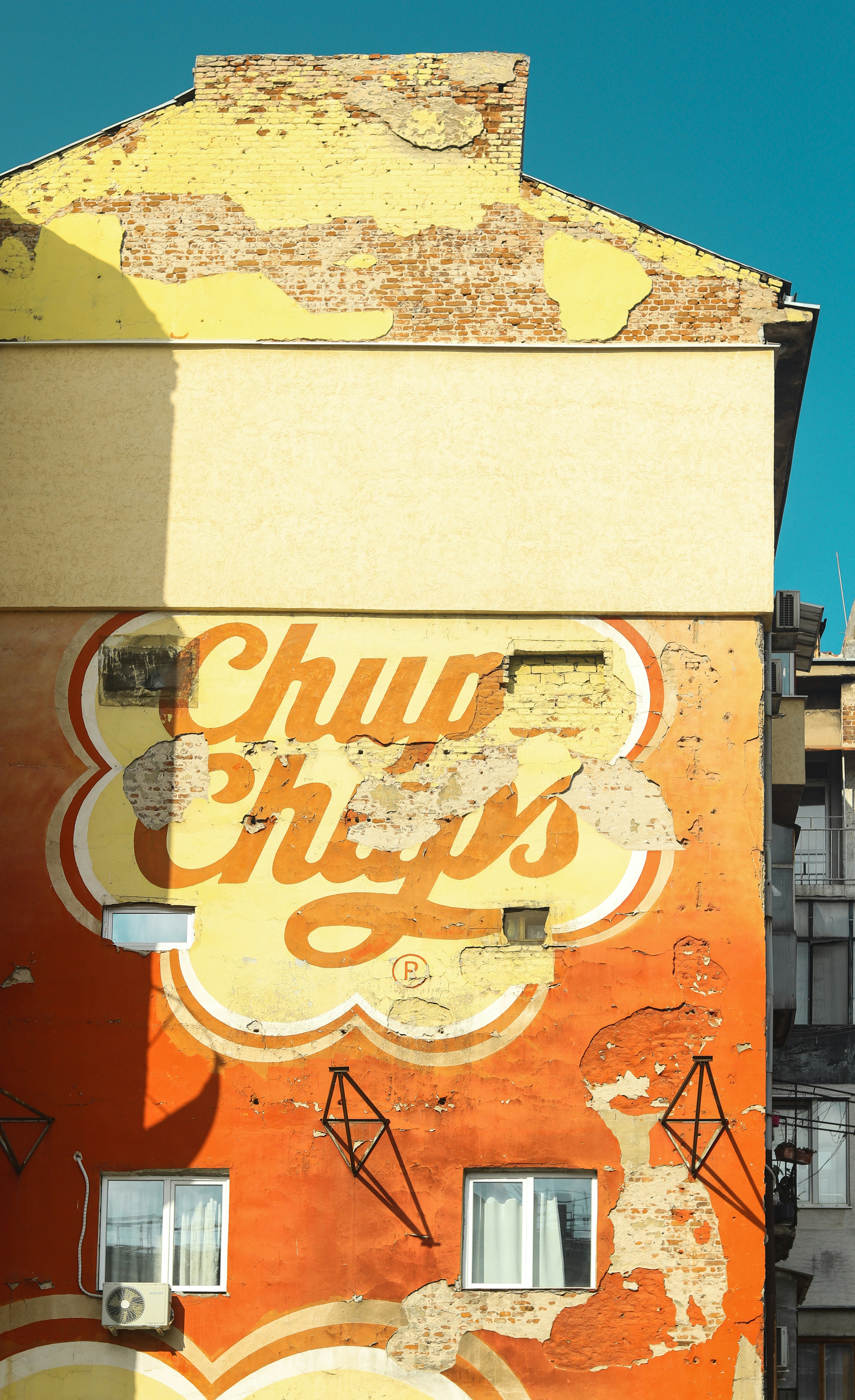 Peeling mural on a sunlit brick building under a crisp blue sky
