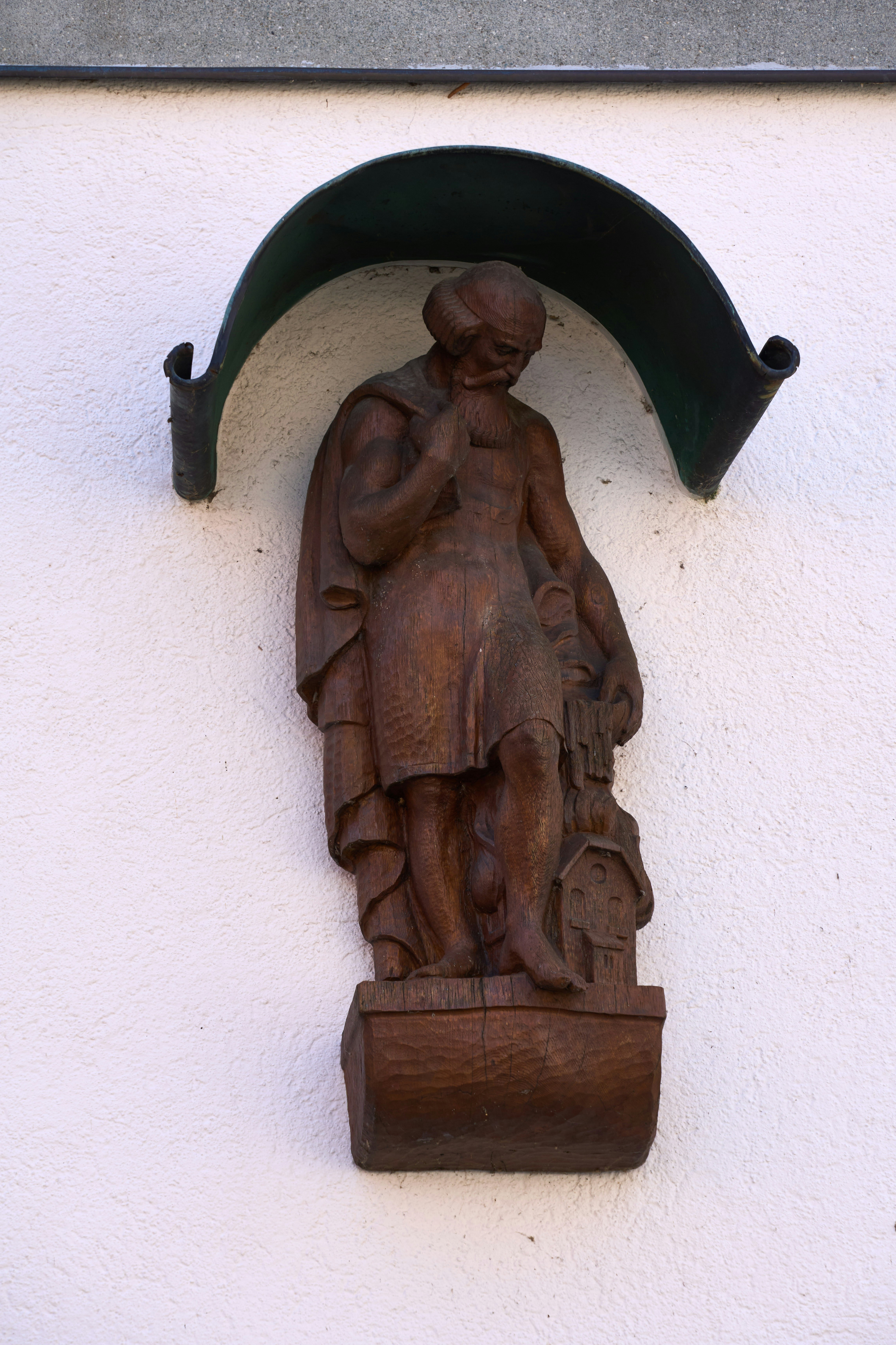 Wooden Saint Under a Green Arch: A Rust-Colored Carved Figure on a White Wall