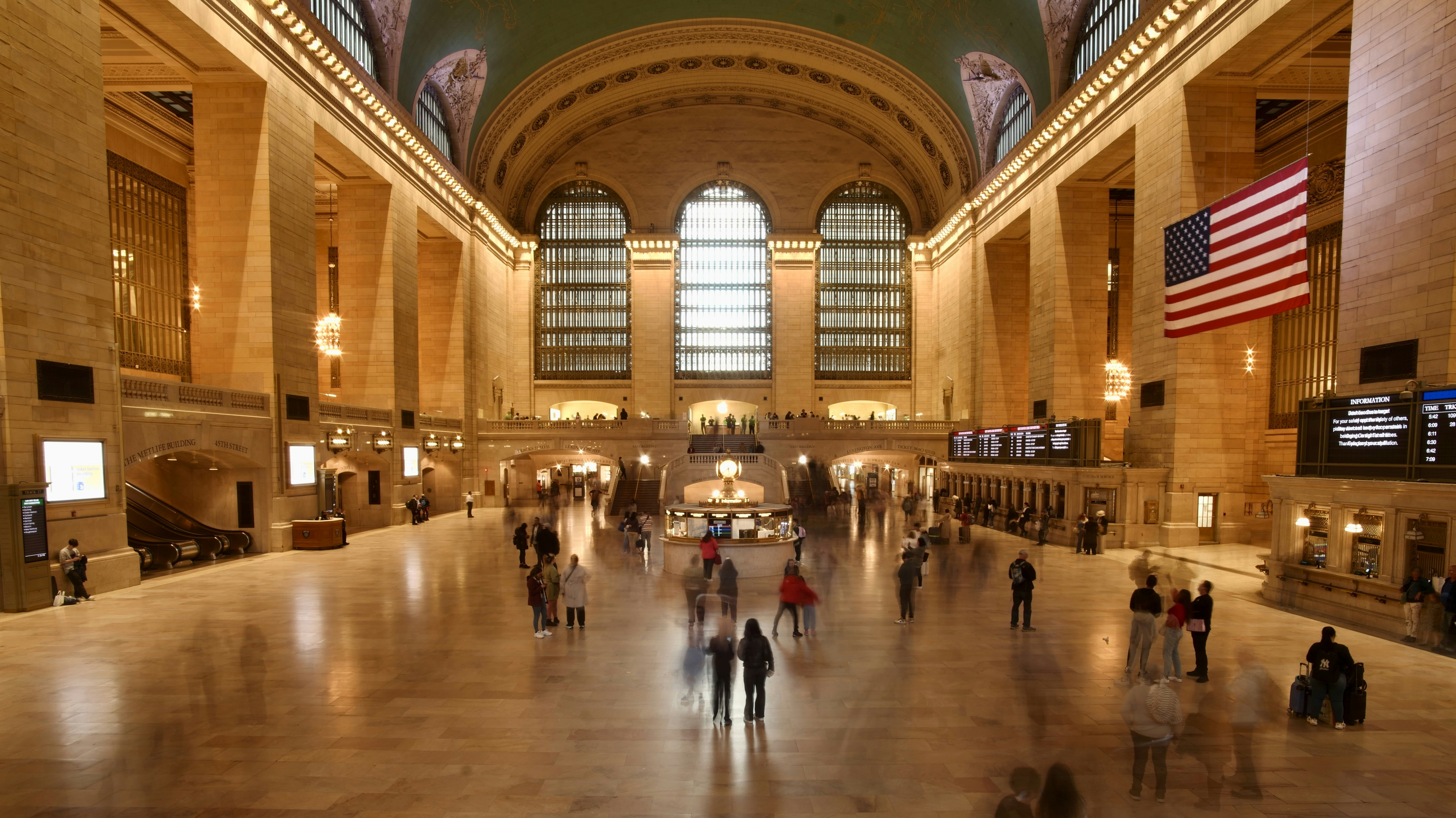 Grand Central Terminal's main concourse with blurred commuters and an American flag.