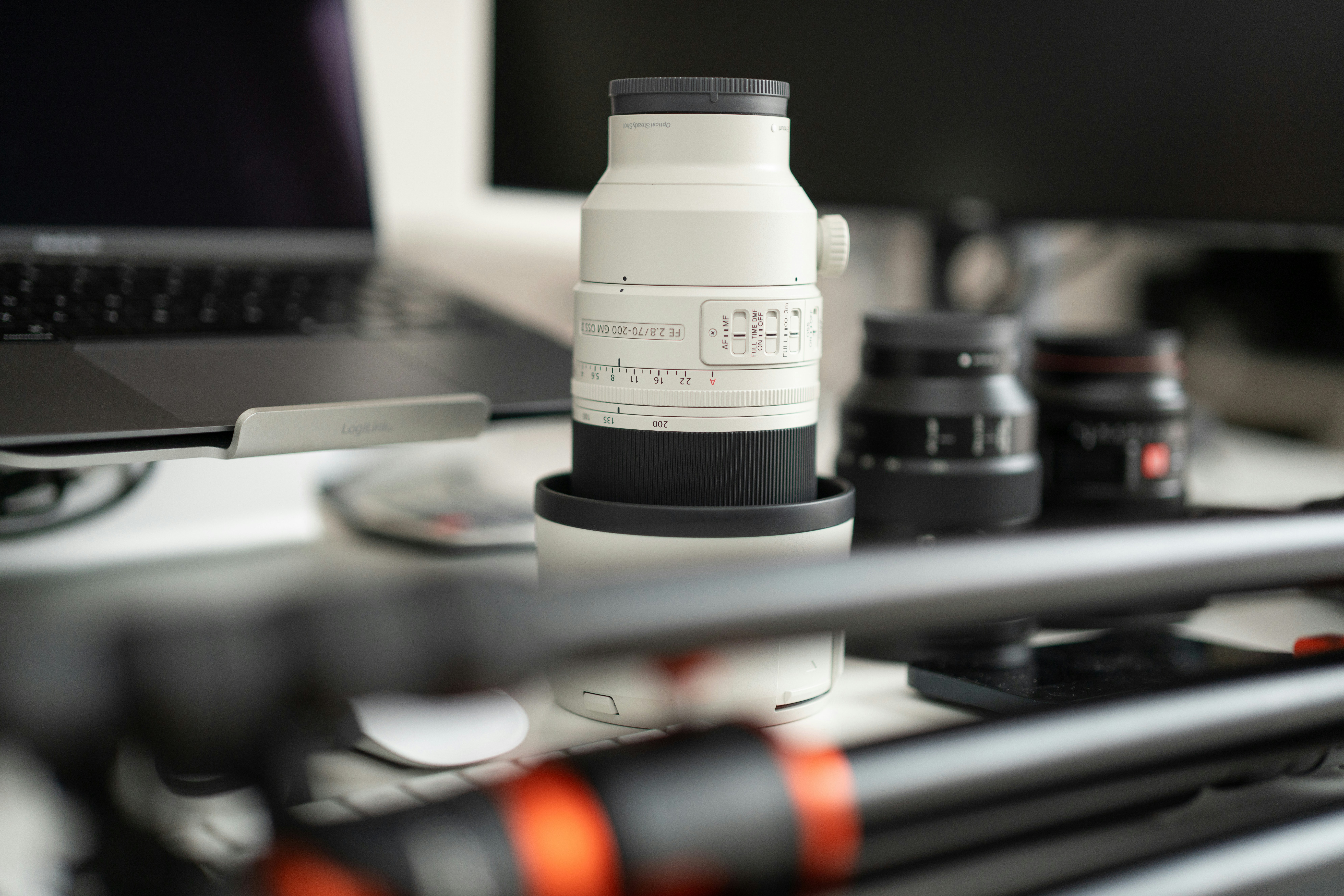 Centerpiece on a Cluttered Studio Desk: A White Telephoto Lens Anchoring the Setup