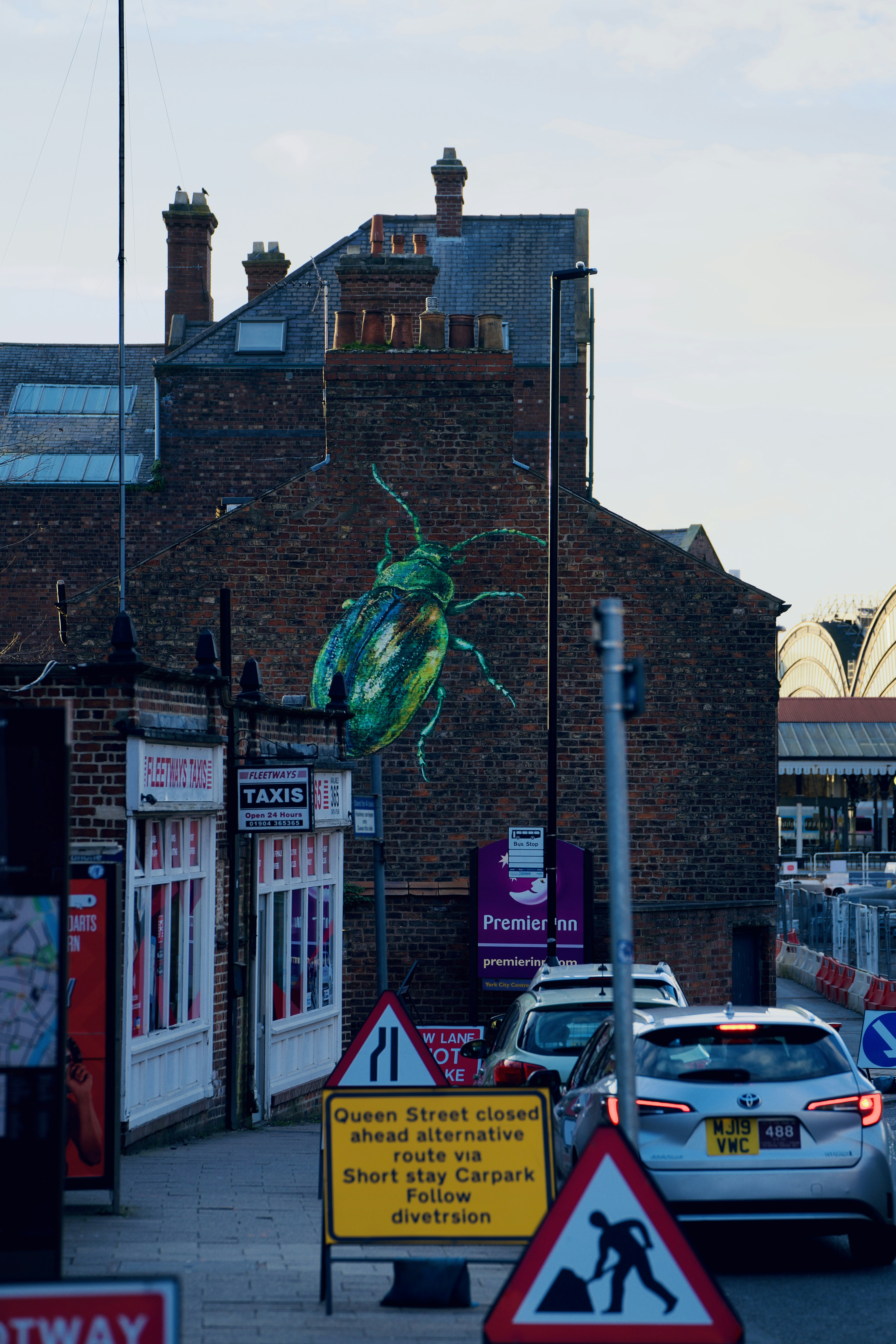 Emerald Beetle on Brick Wall: A Street-Side Mural Commands the Lane