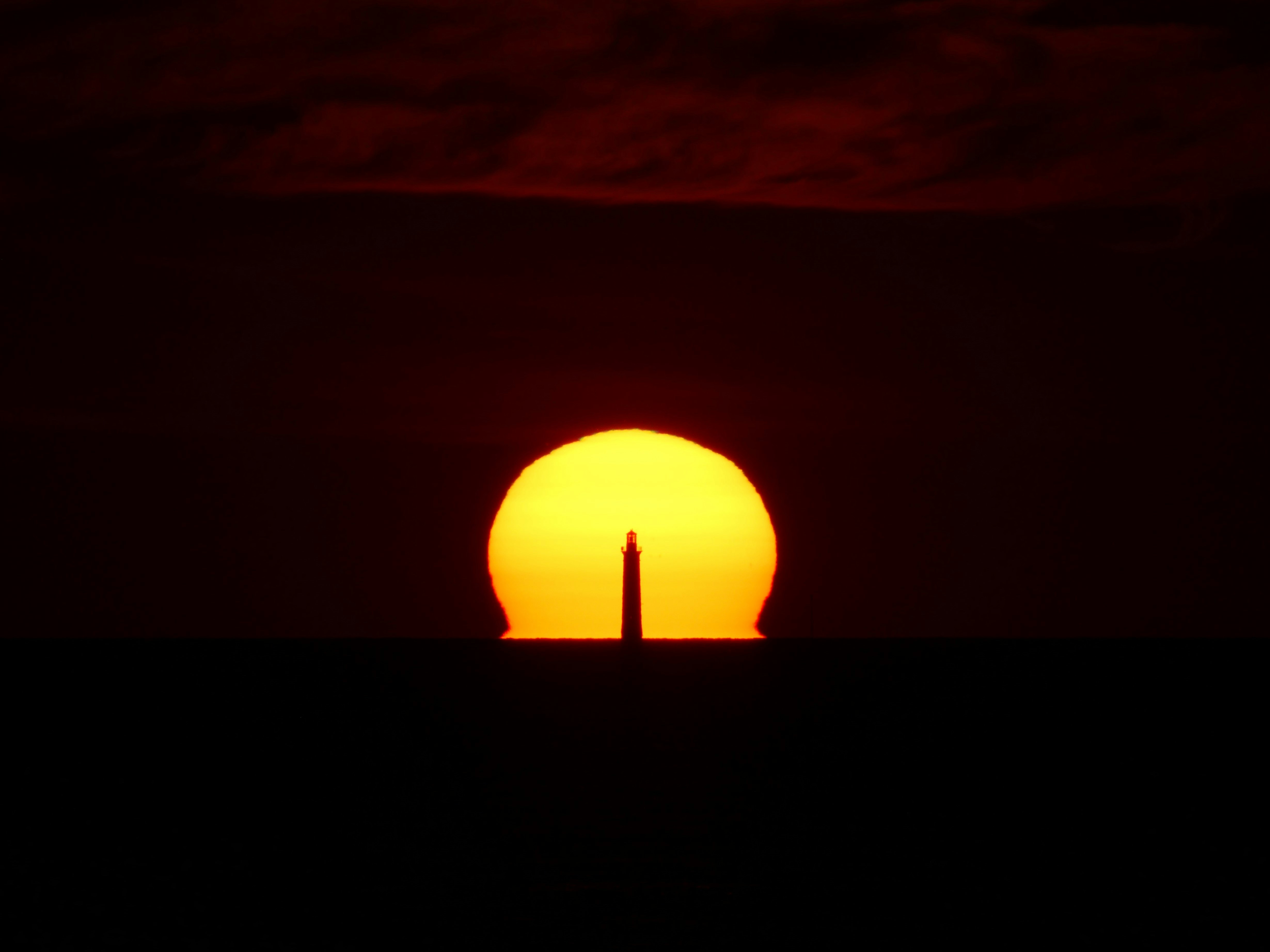 Dawn's Sentinel: The Sun Aligns with a Lone Lighthouse