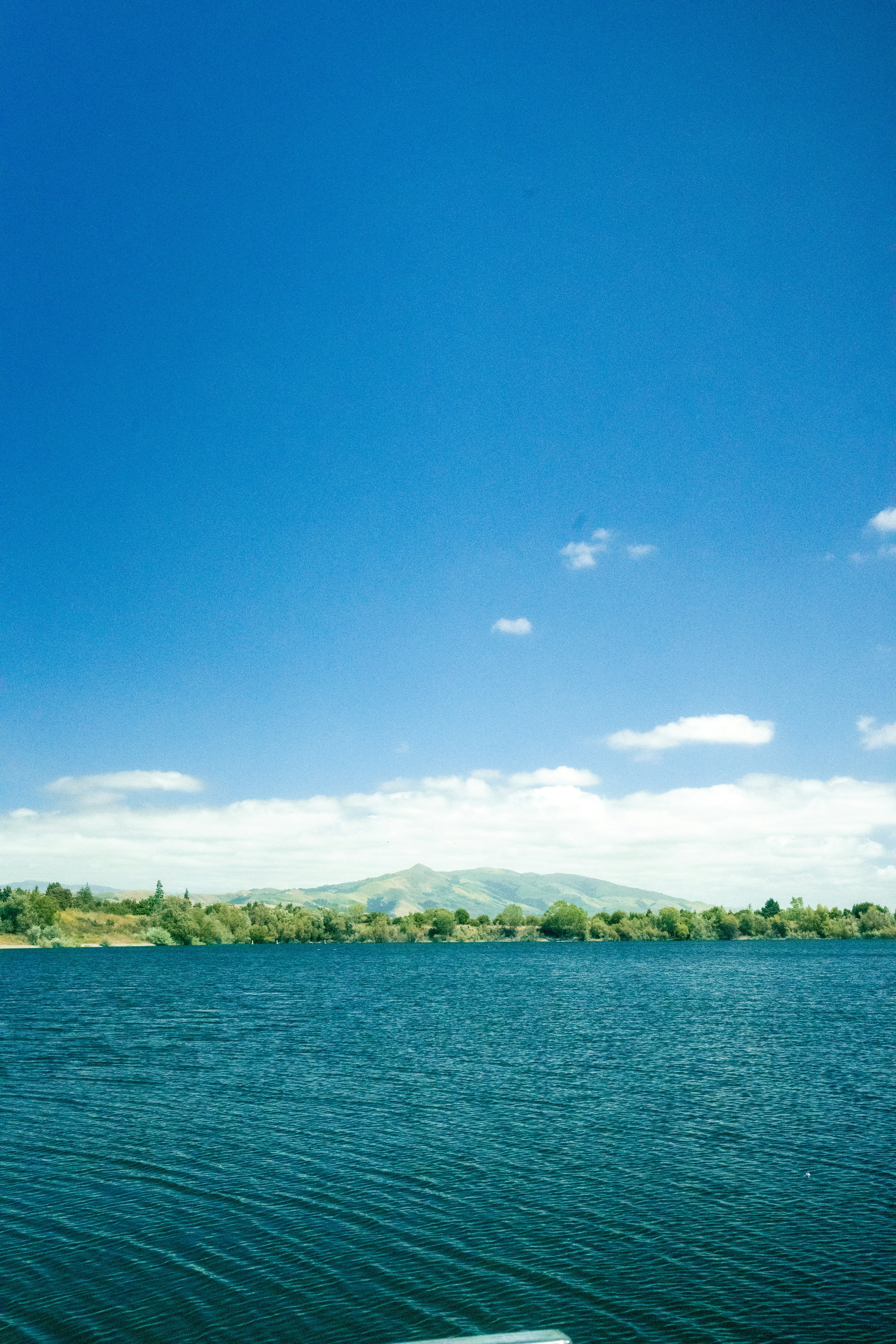 Lush green hills rise gently against a clear blue sky, reflecting on the tranquil surface of a lake.