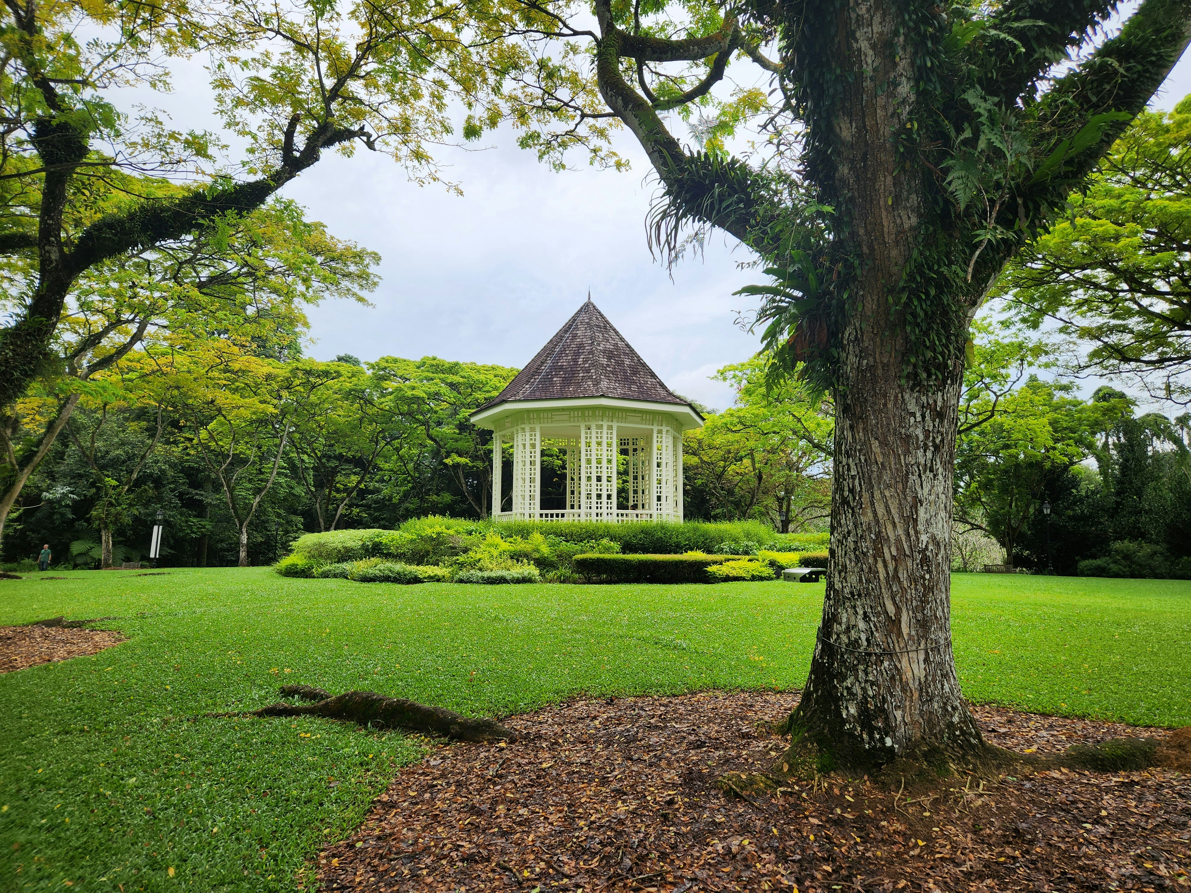 Charming garden pavilion surrounded by lush greenery and trees, offering a tranquil escape. The structure's elegant design complements the natural landscape.