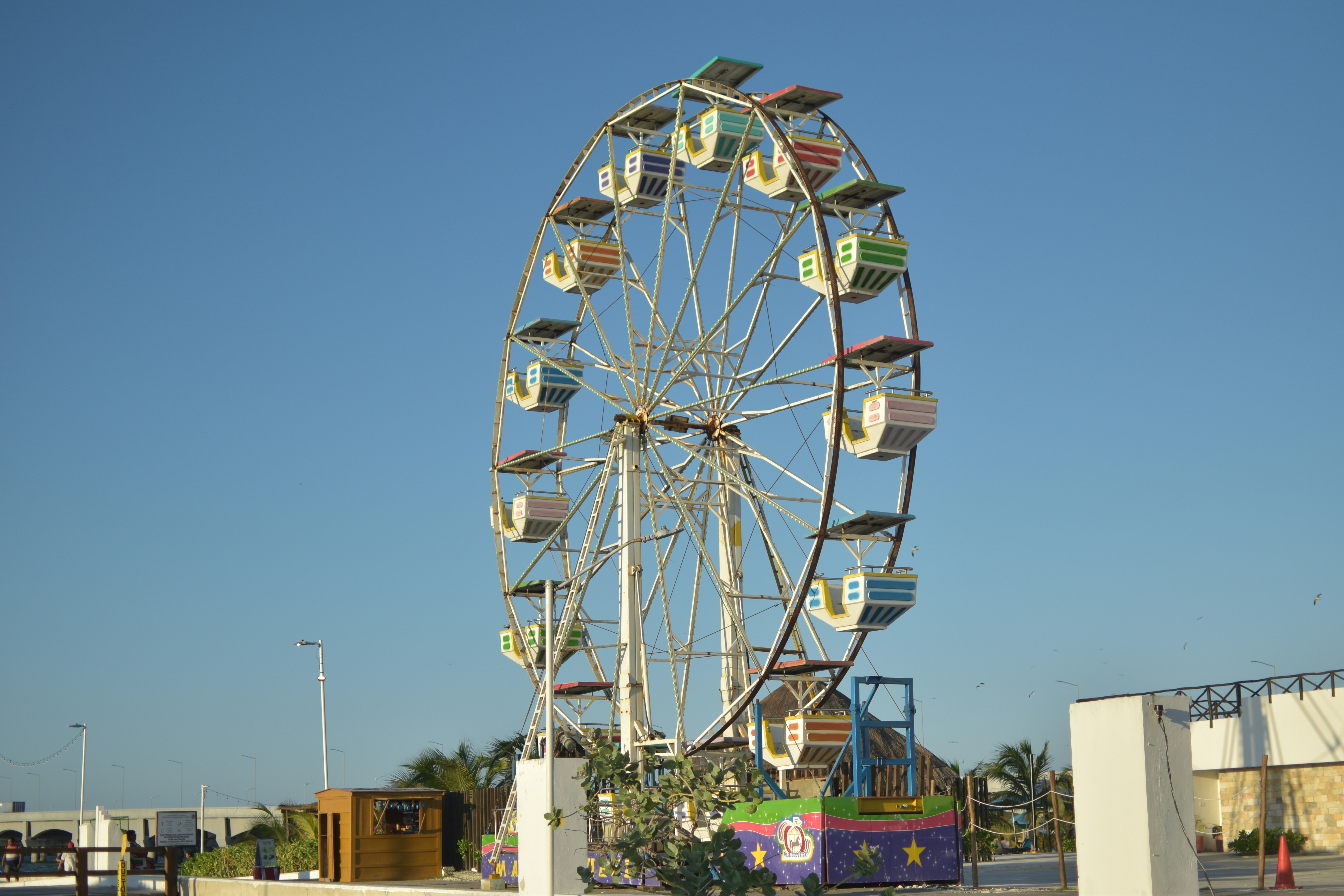 Pastel Cabins in Motion: A Ferris Wheel Framing a Sunny Fairground
