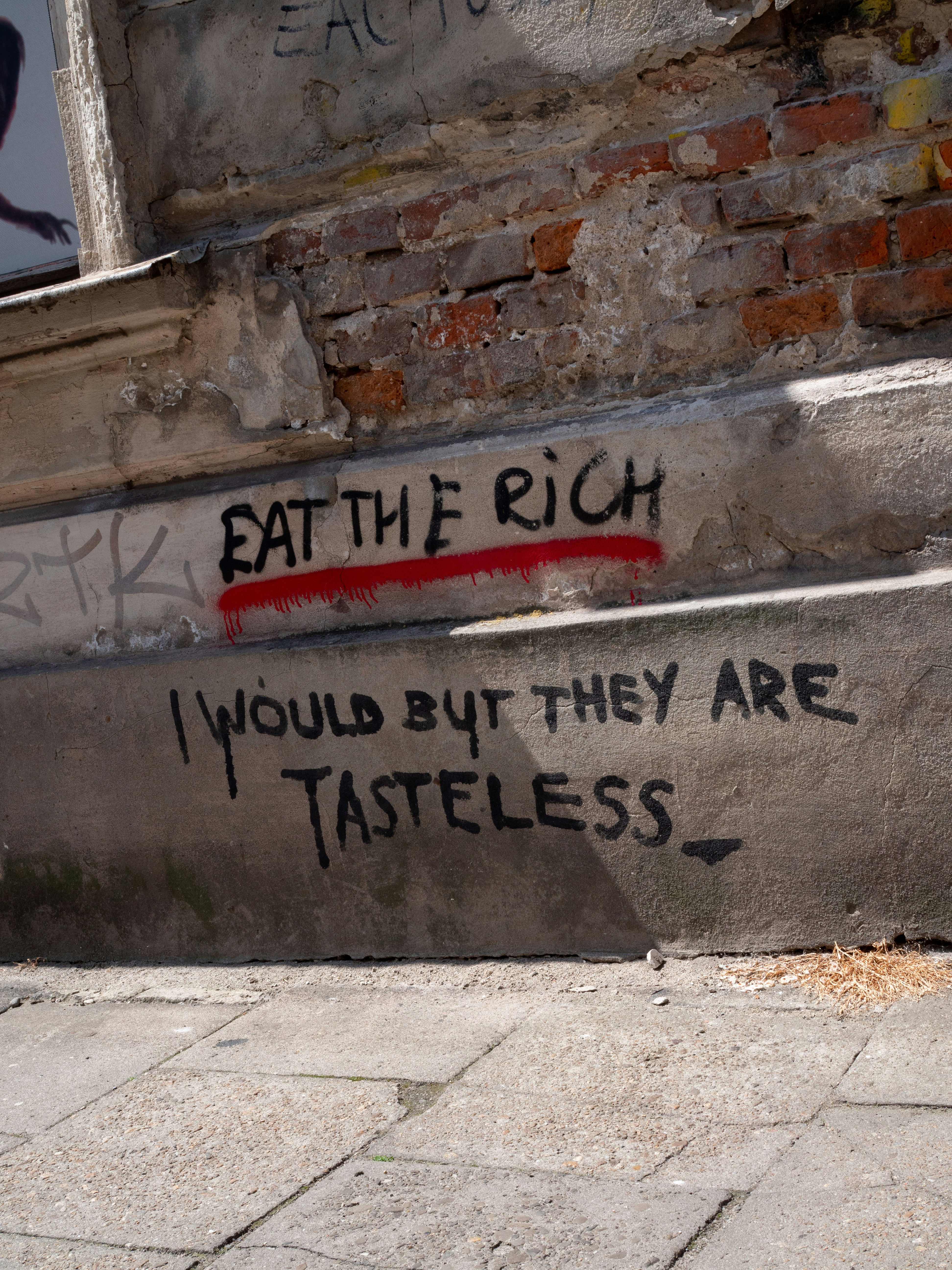 Graffiti on a weathered wall features a satirical message about wealth disparity. The juxtaposition of bold lettering against the crumbling surface adds to its impact.