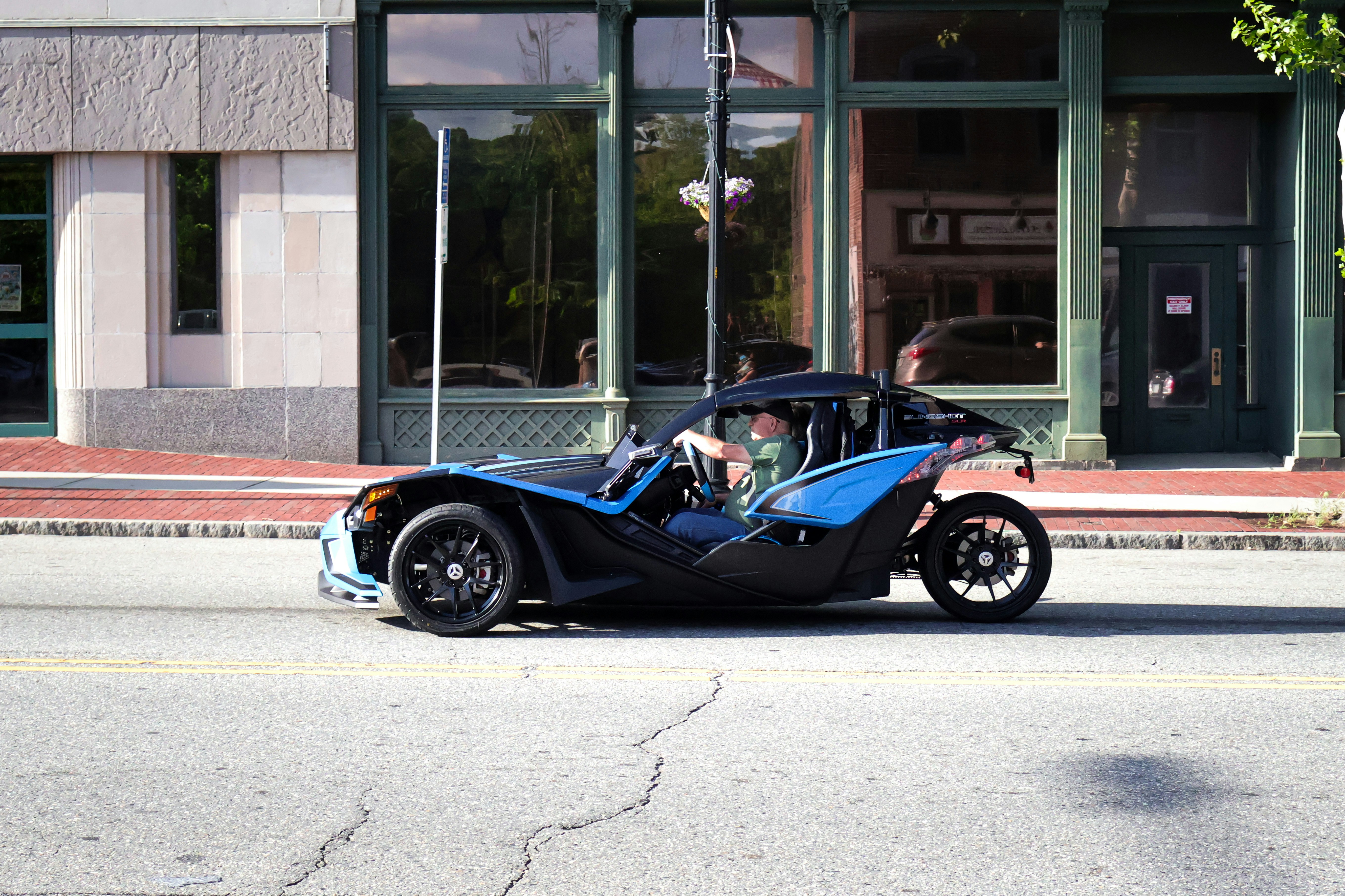 Three-wheeled vehicle cruising on a city street against a backdrop of storefronts.