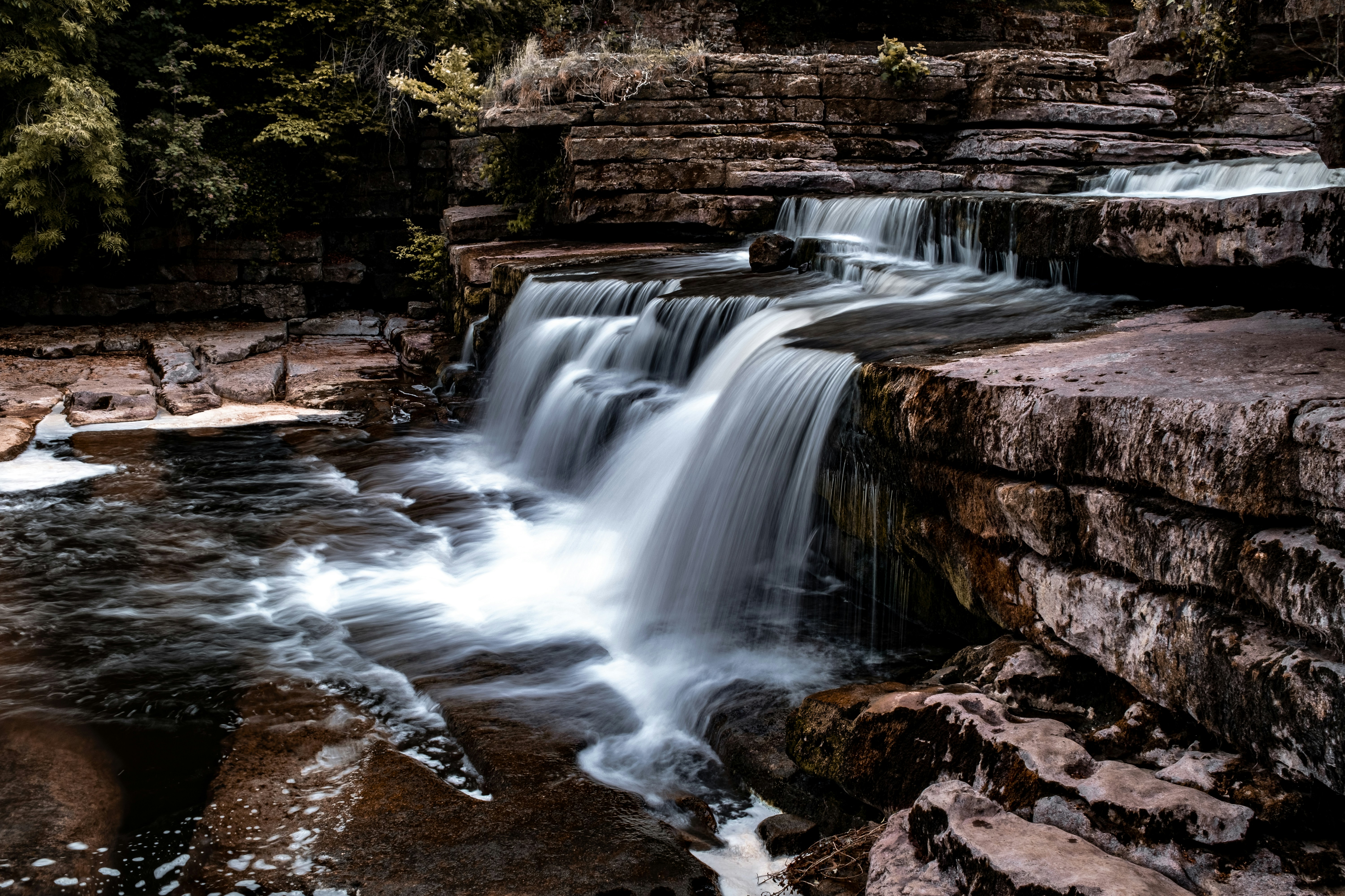 Water cascading over layered rock formations in a tranquil forest setting.