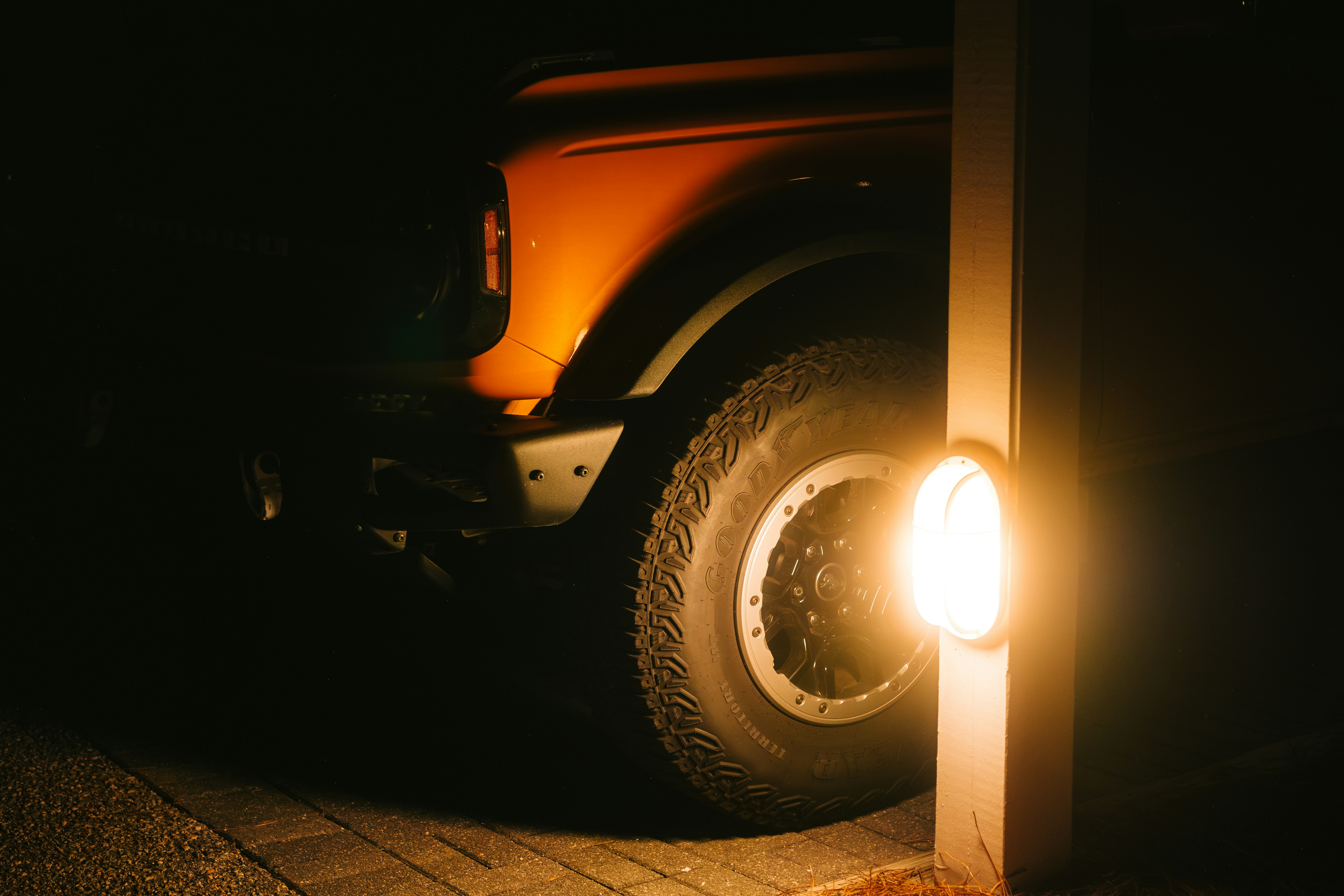 A Ford Bronco with its side profile lit by a small lamp on a post