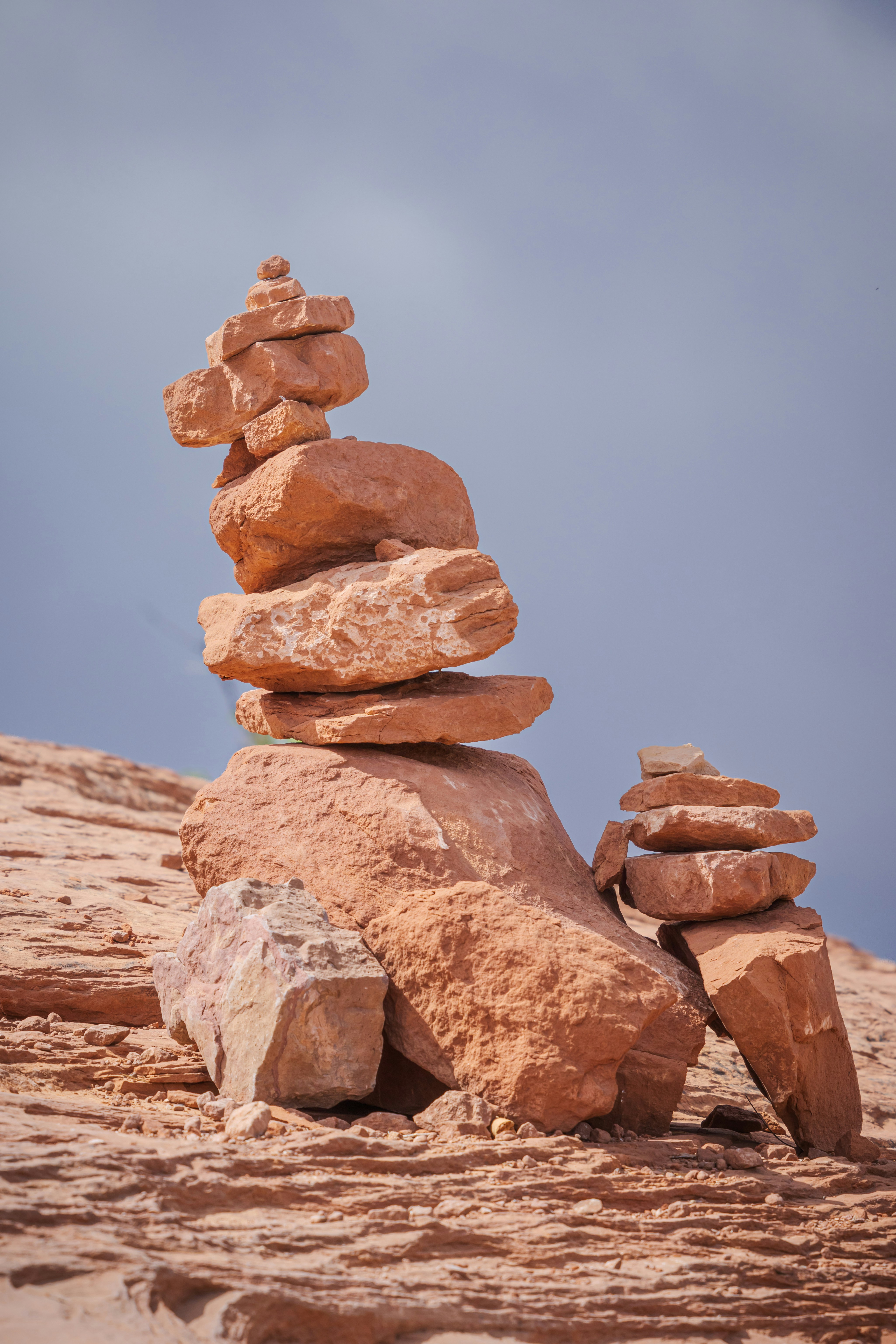 Desert Cairns: A Vertical Stack of Rust-Red Stones Against a Pale Blue Sky
