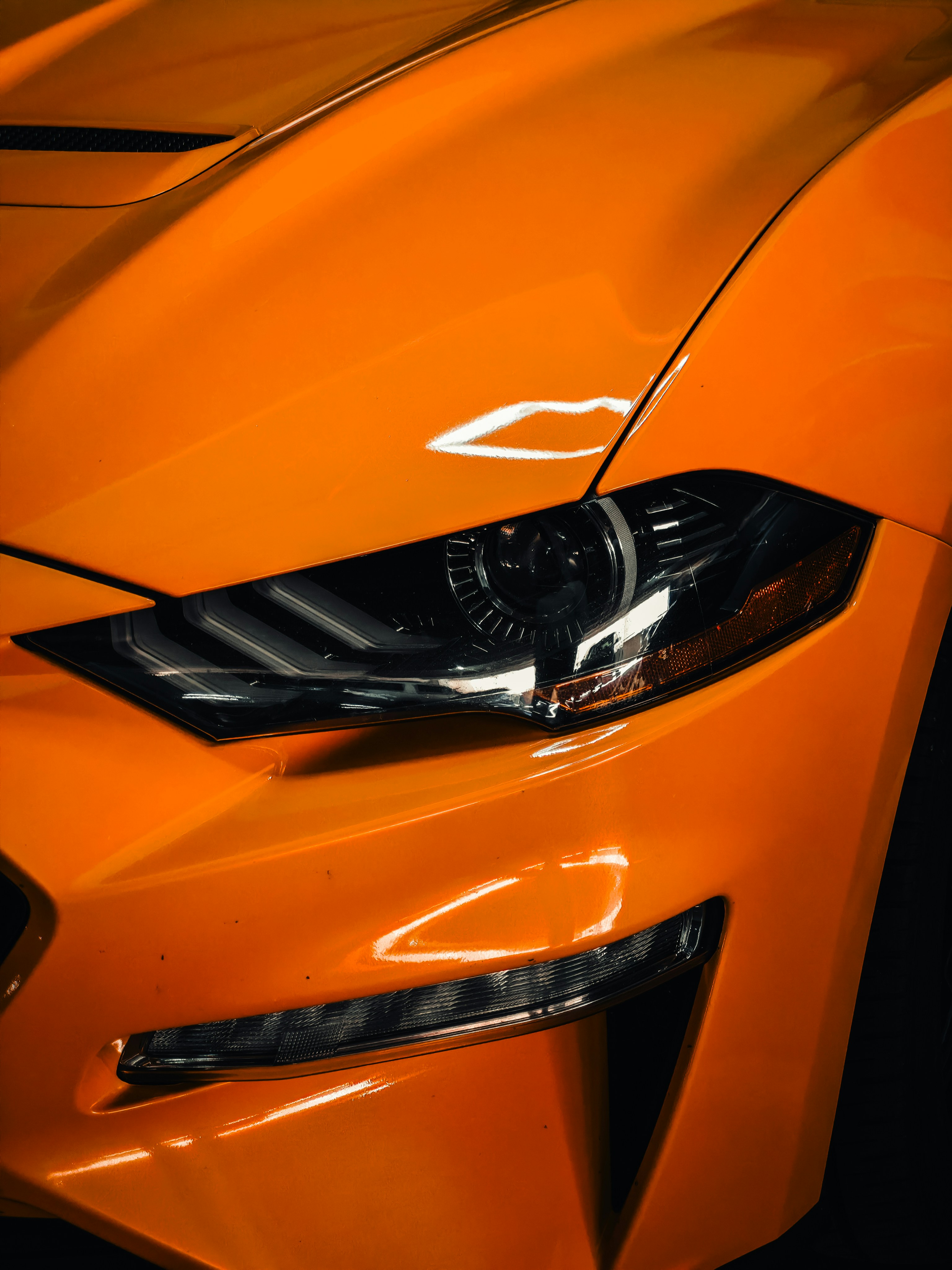 Close-up of a sleek orange sports car's headlight and hood, showcasing intricate design and craftsmanship.