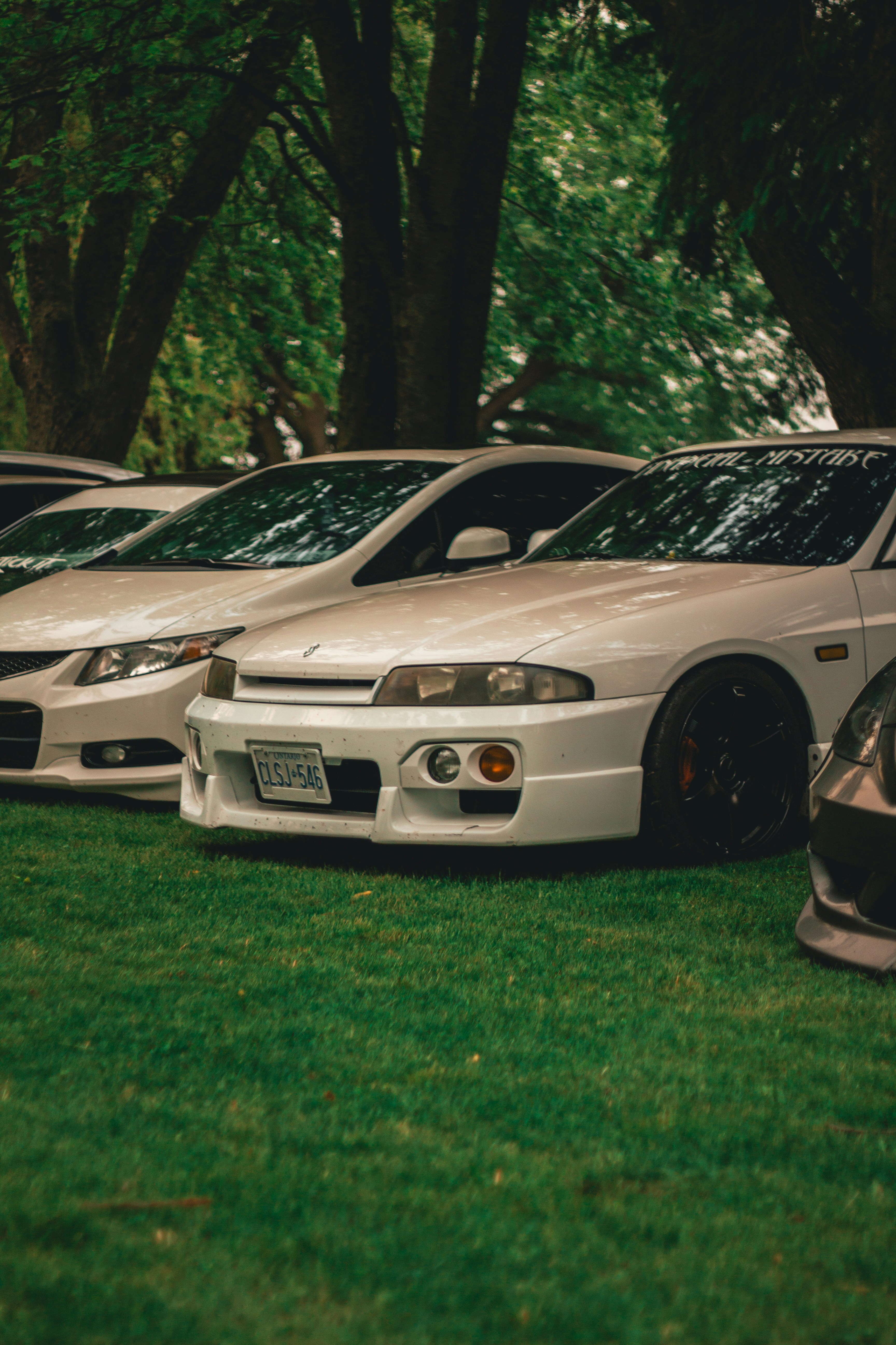 A row of parked cars sitting on top of a lush green field photo – Free ...