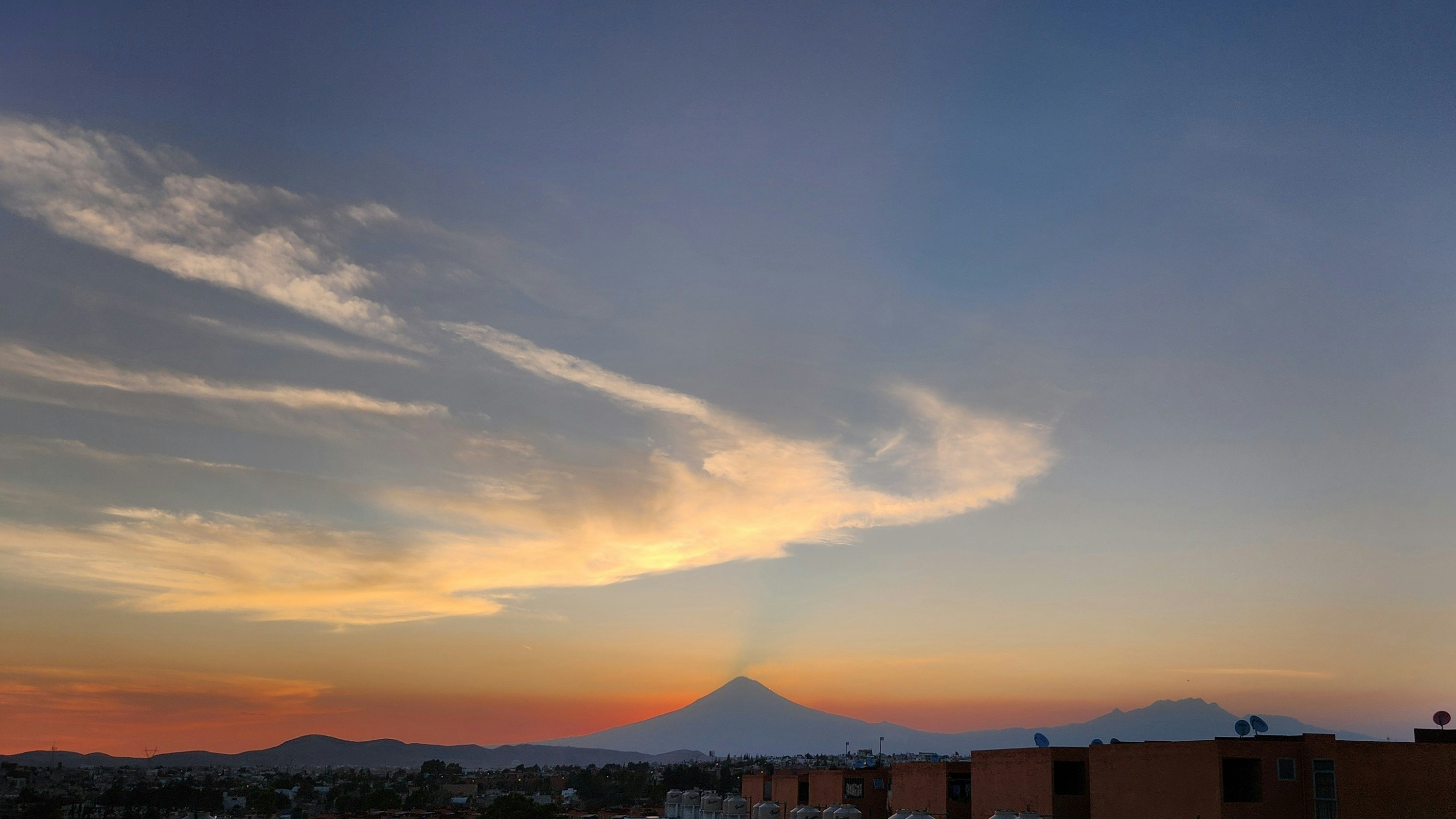 Sunset casting warm hues over a cityscape with a prominent mountain silhouette in the background.