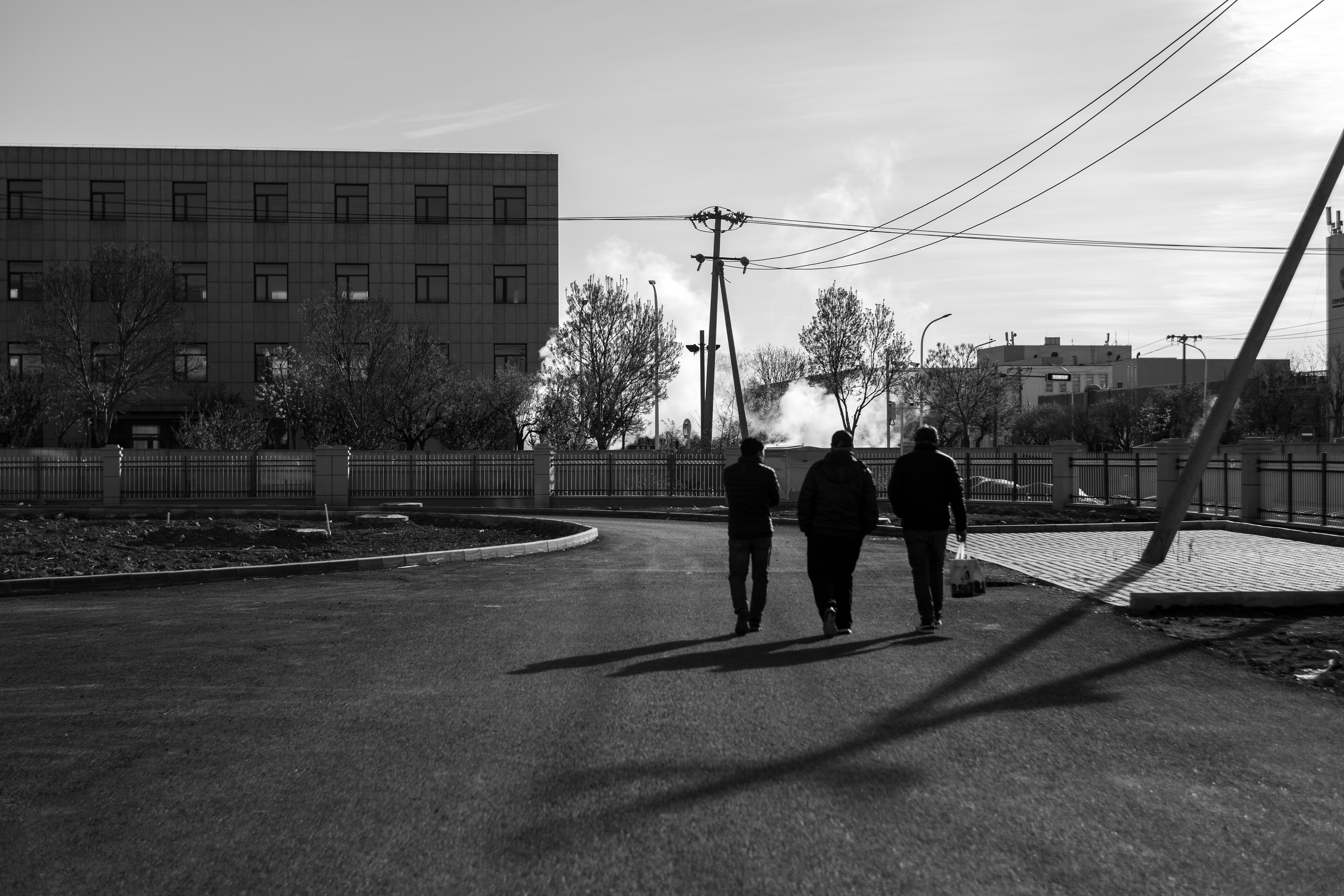 Three Silhouettes Trek Across a Sparse Industrial Street
