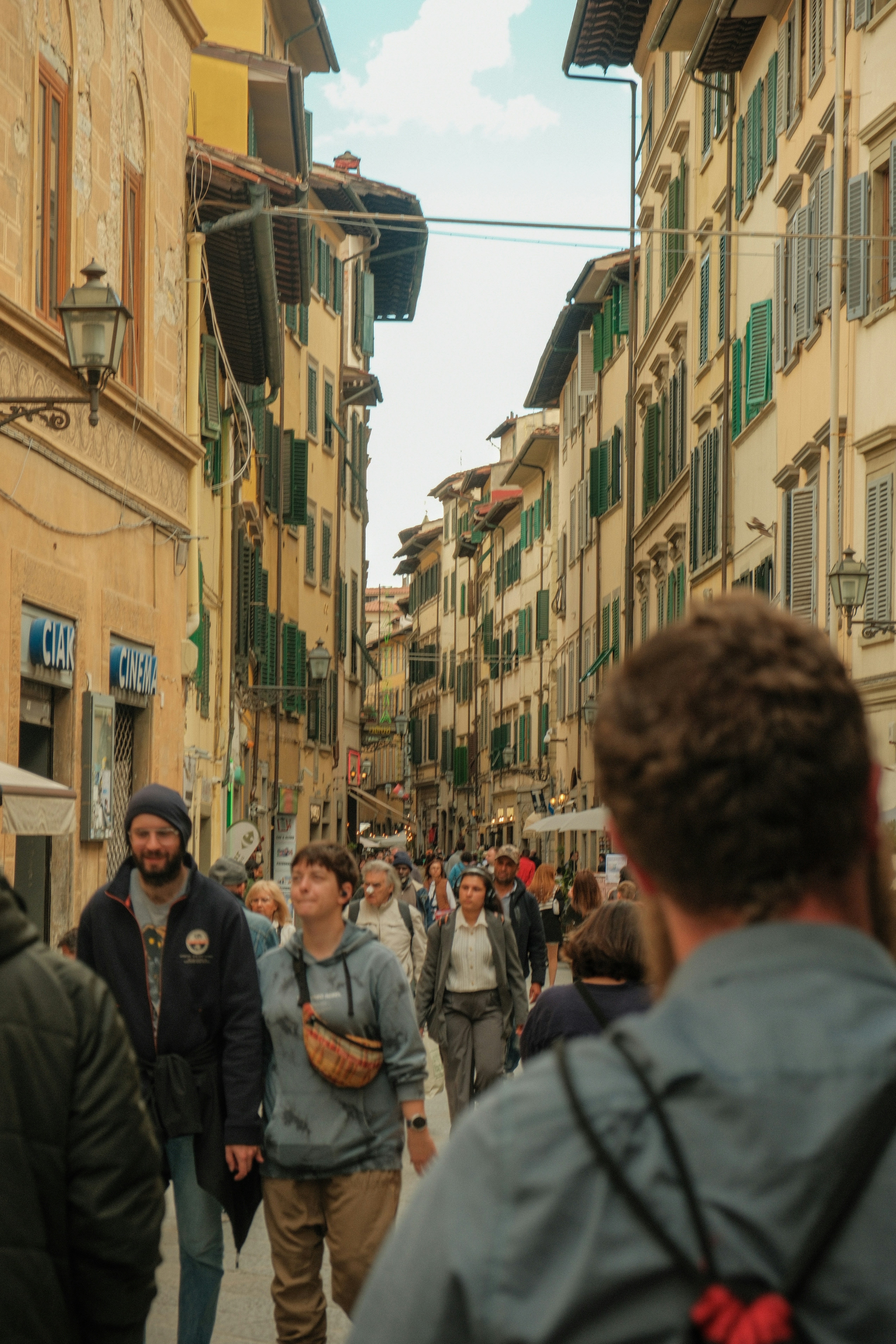 Sunlit Calle: Crowds Move Through a Narrow Italian Street