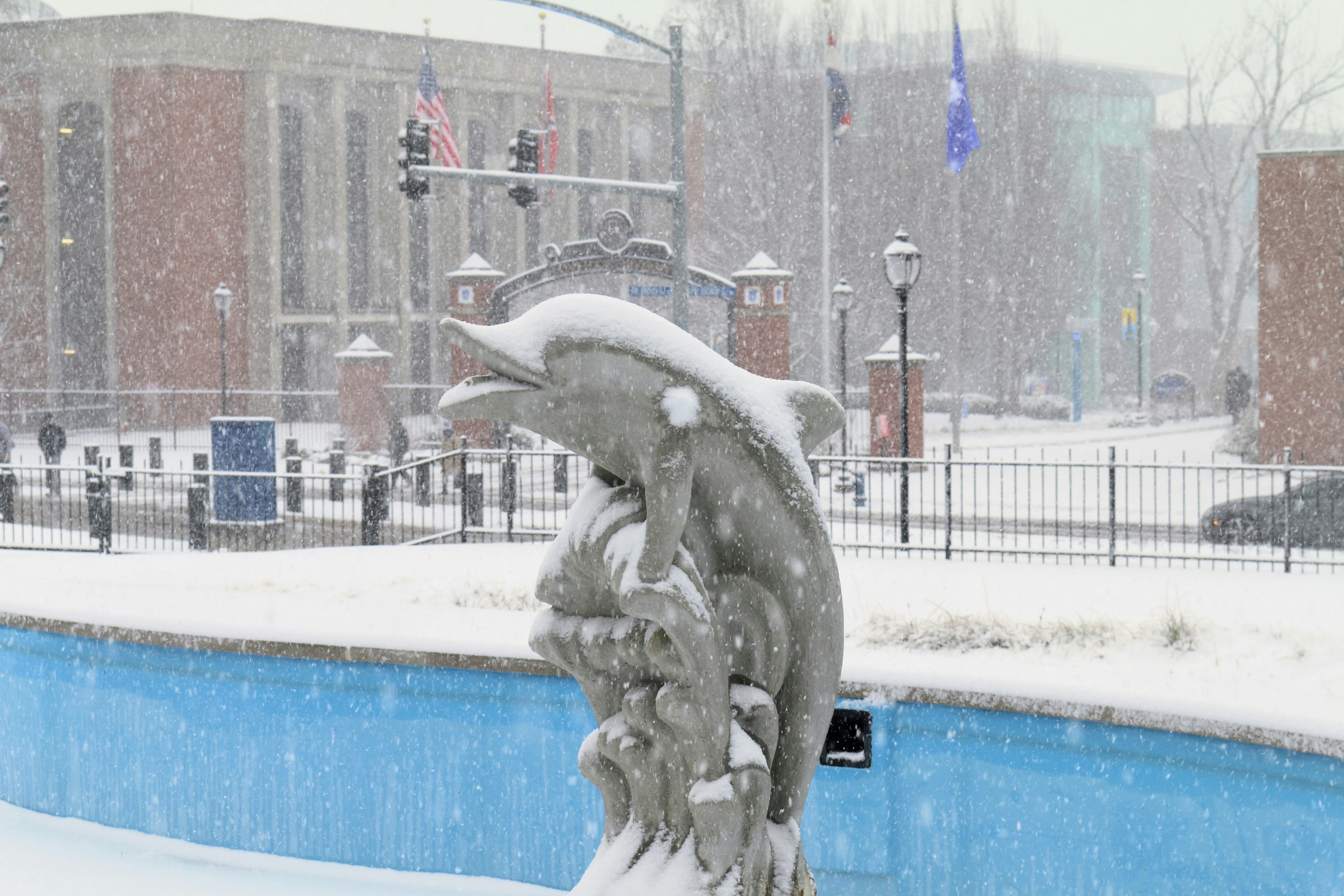 Winter's Sentinel: Snow-Covered Dolphin Statue Over a Frozen Blue Pool