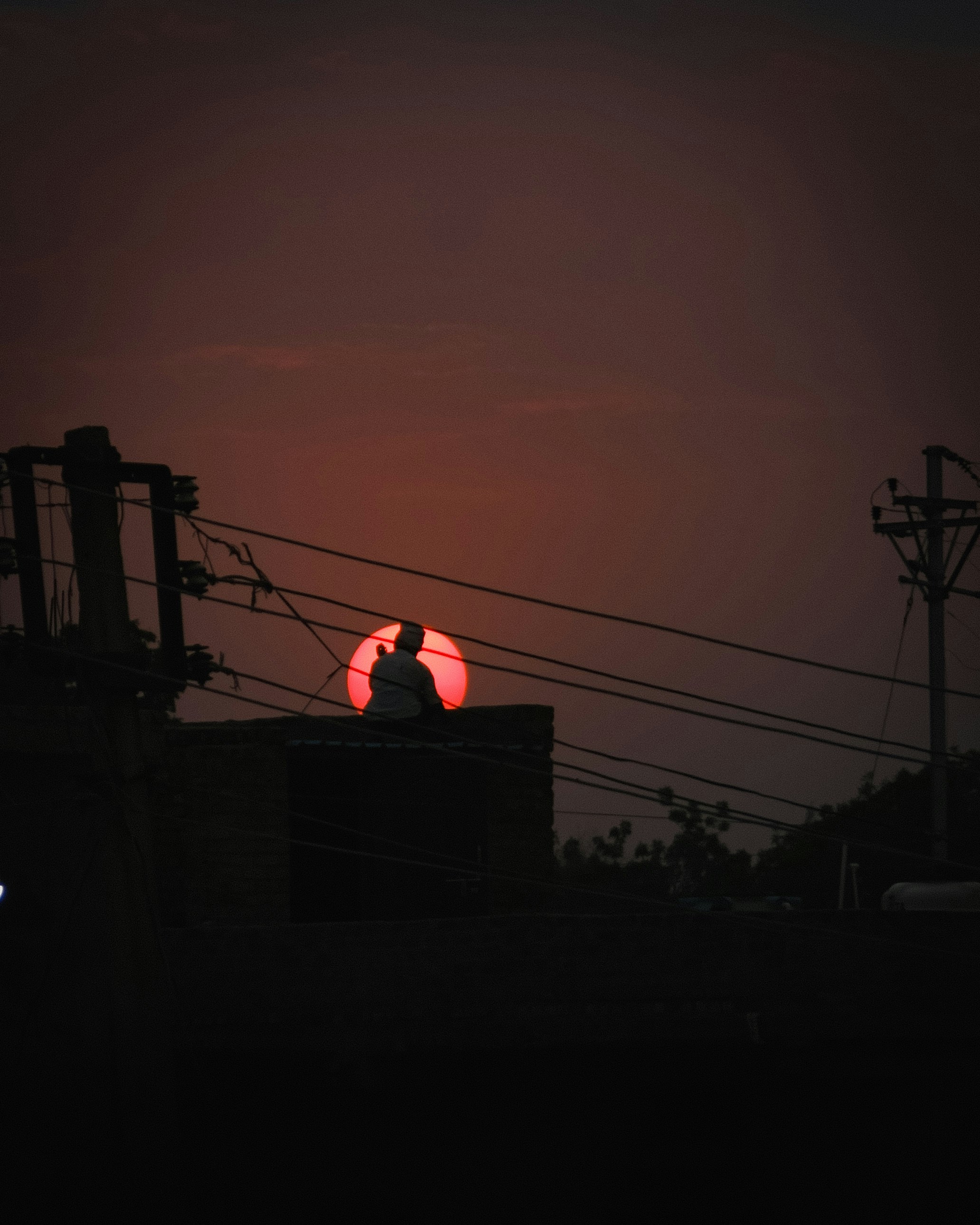 Red Sun Anchored by Rooftop Silhouette Beneath a Web of Power Lines