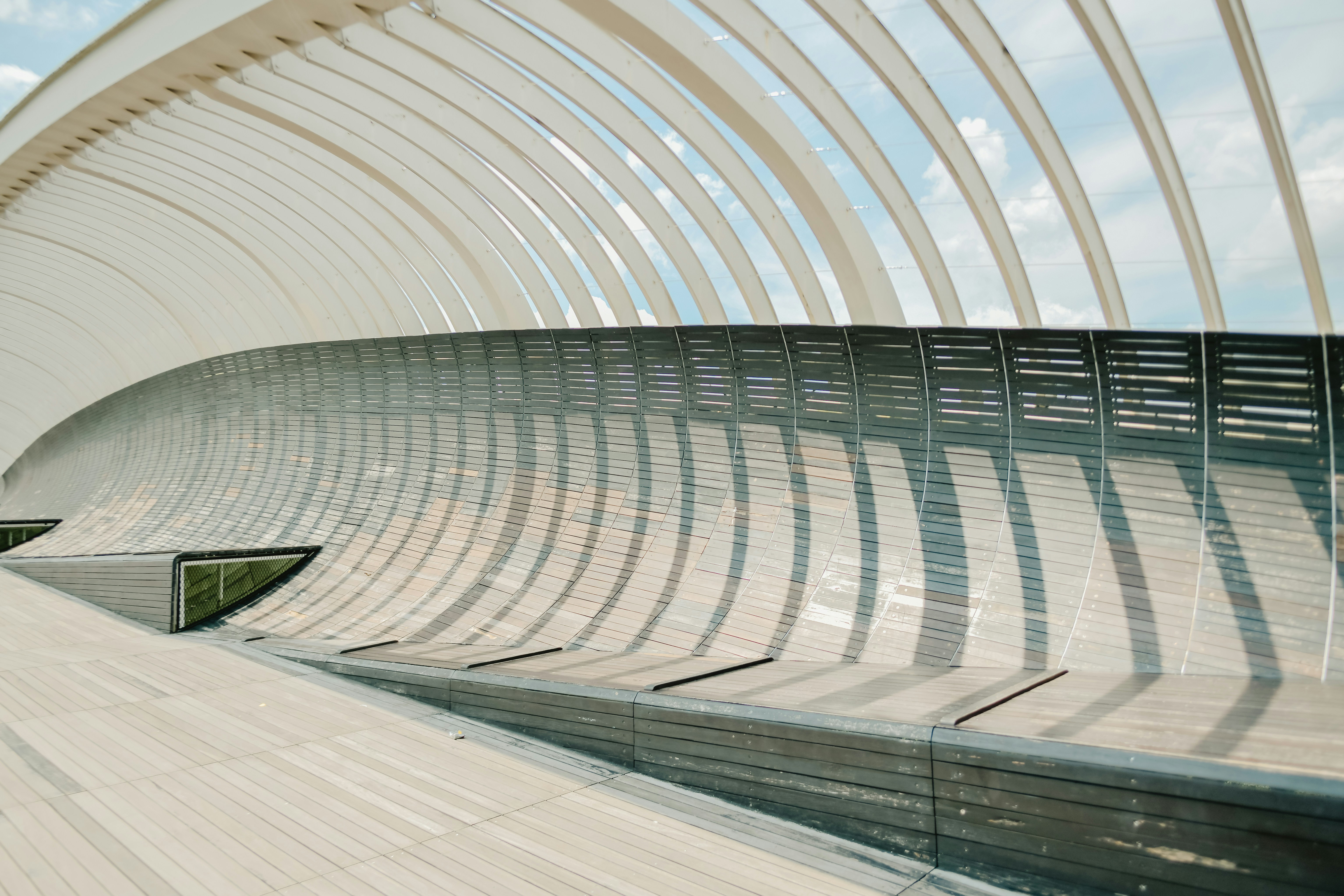 Curved architectural structure with a series of arches set against a partly cloudy sky.