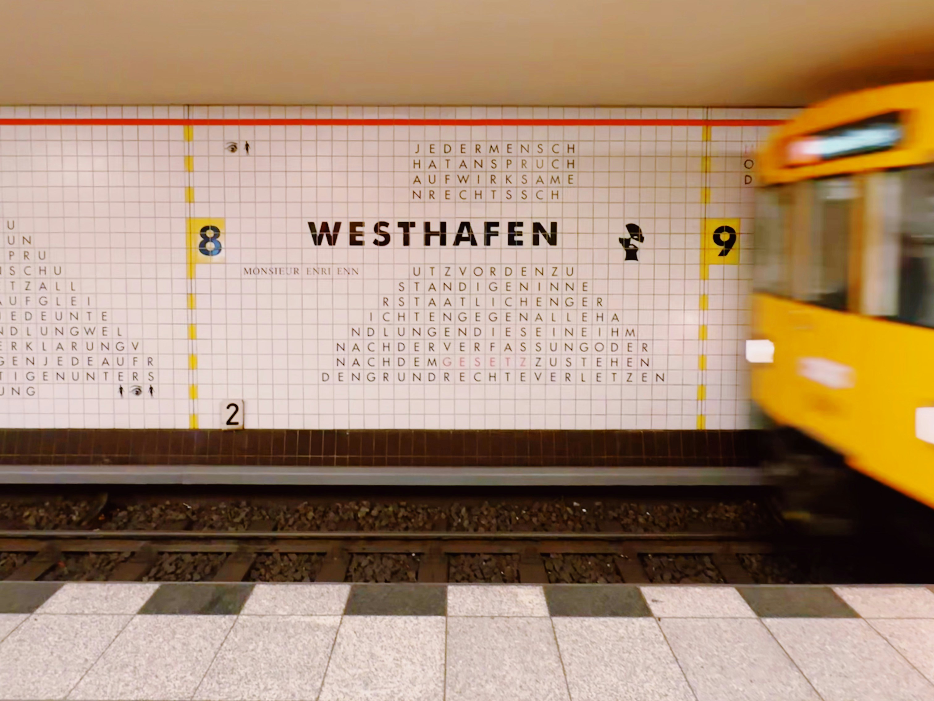 Westhafen Station: A Yellow Train in Motion Across a Quiet Tiled Platform