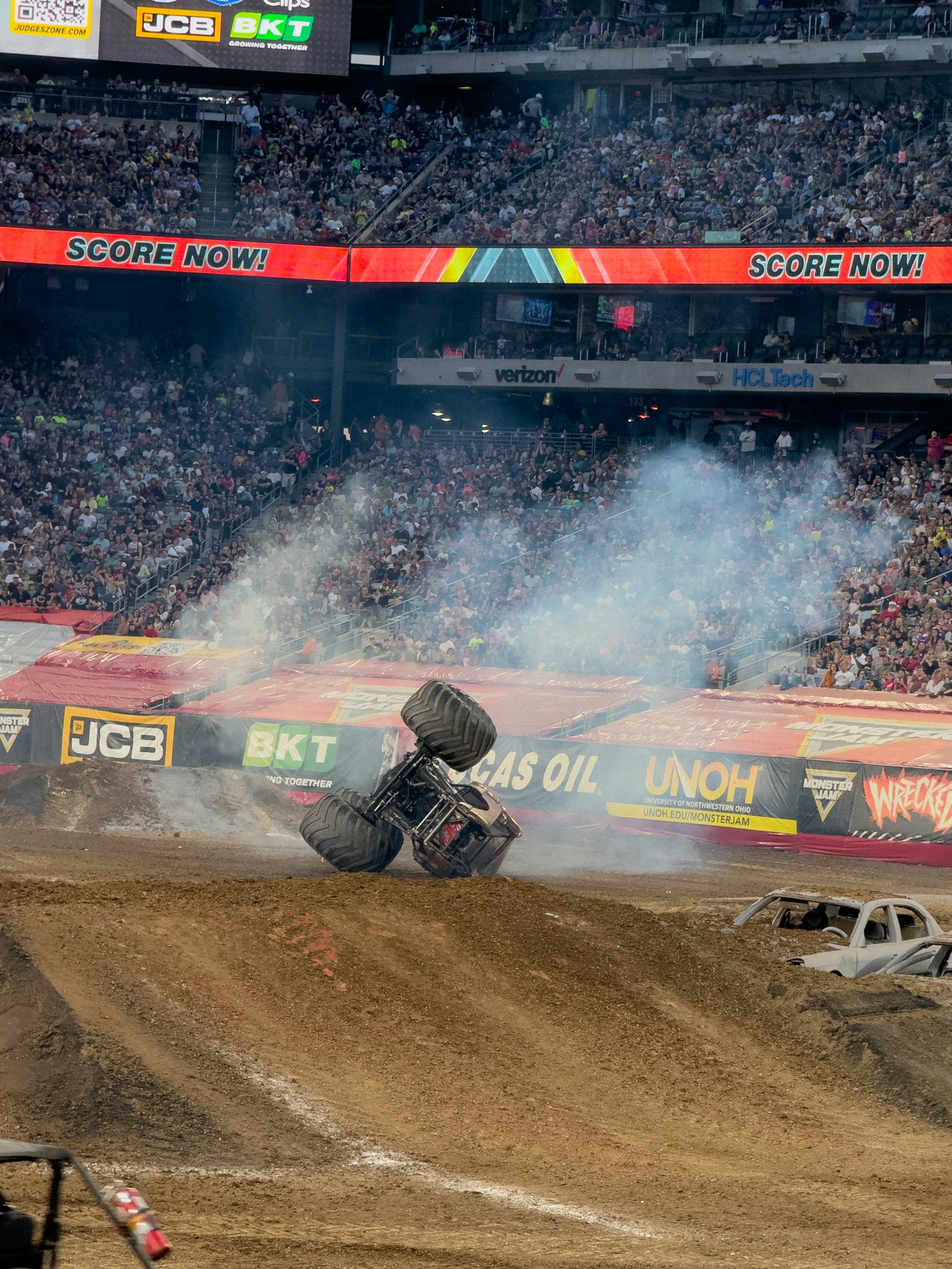 Monster truck performing a dramatic flip amidst a cloud of smoke at a packed stadium event.