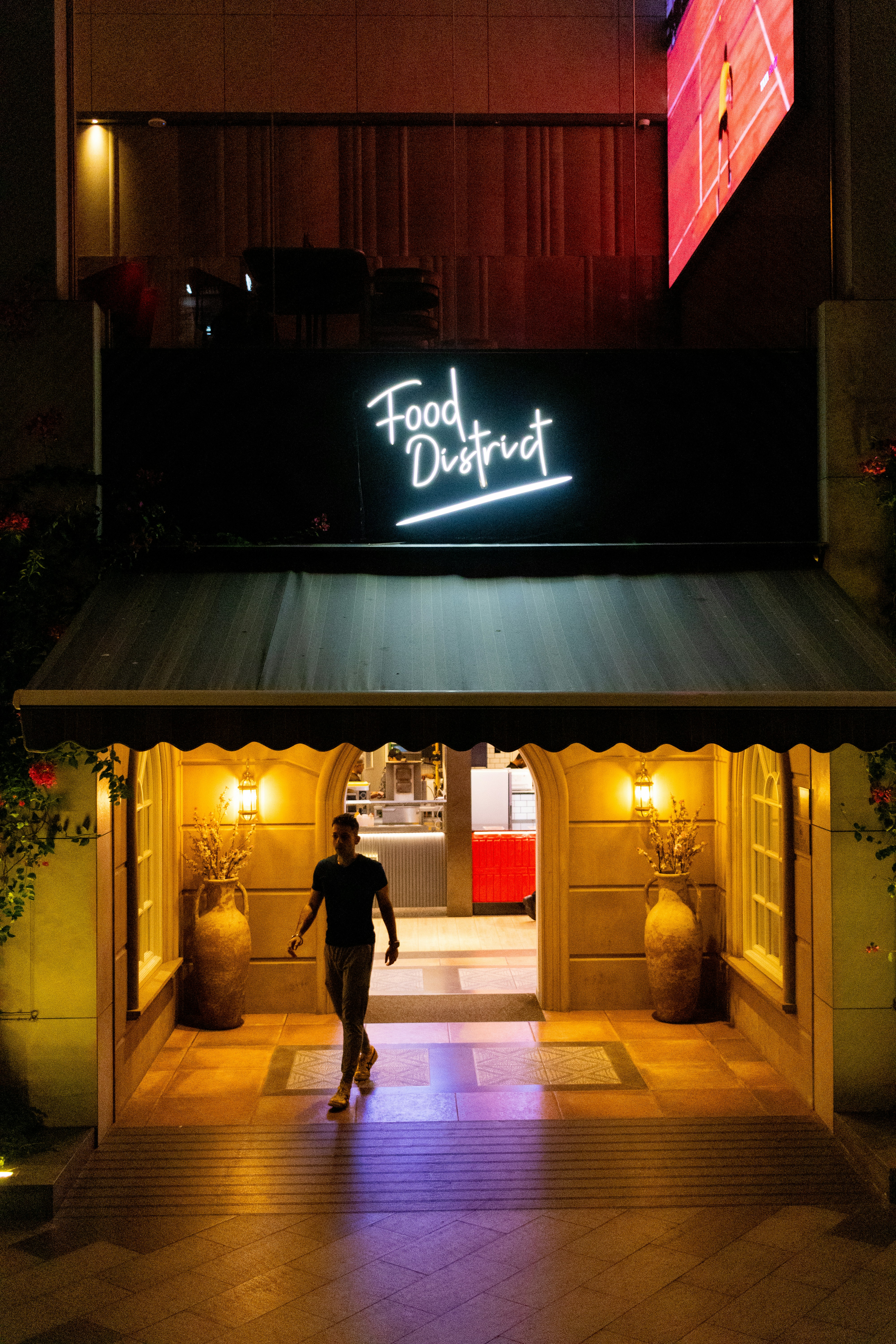 Night entrance to Food District: A lone figure exits a warmly lit restaurant under a neon sign