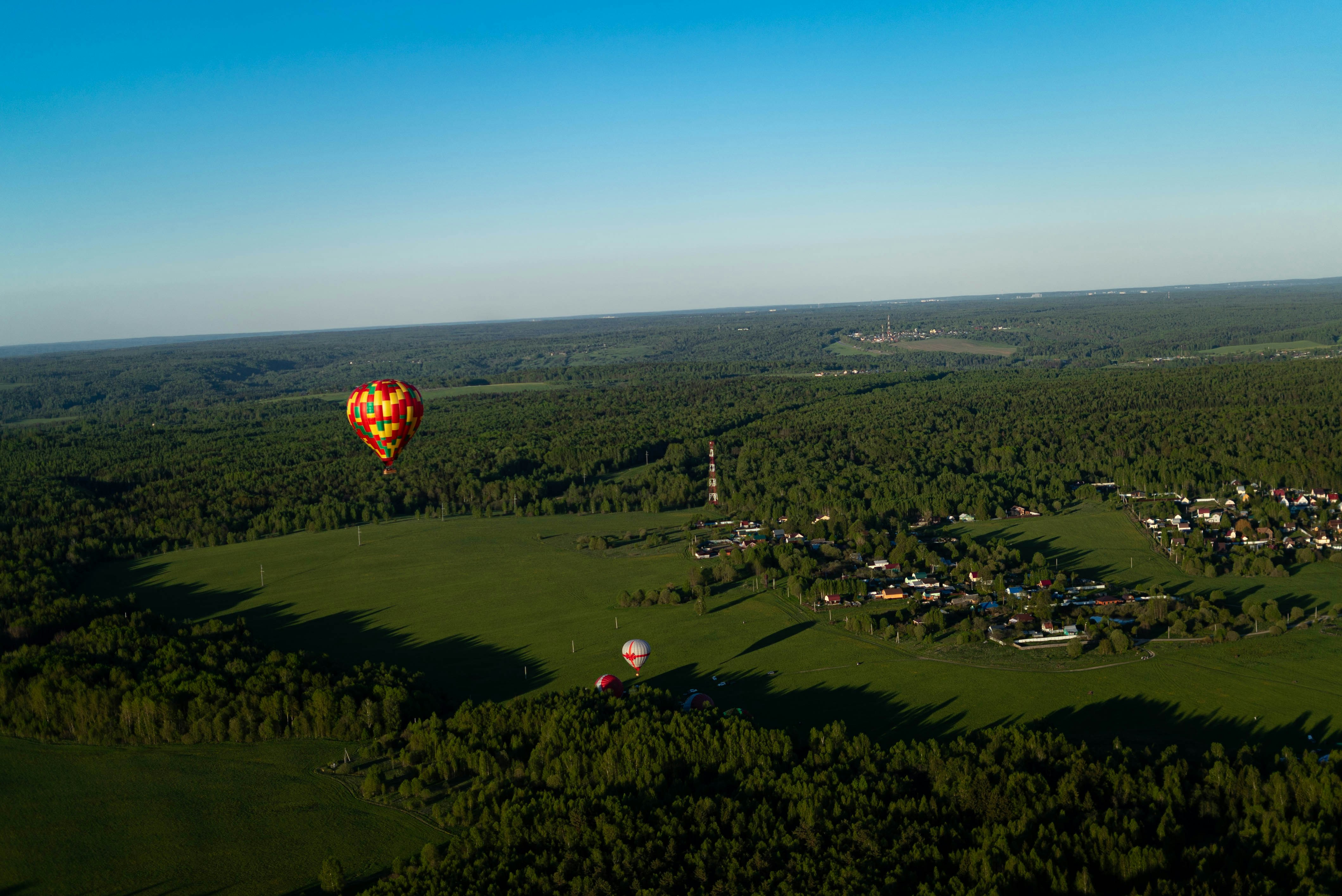 Red-Gold Balloon Drifts Over Verdant Patchwork Below a Clear Sky