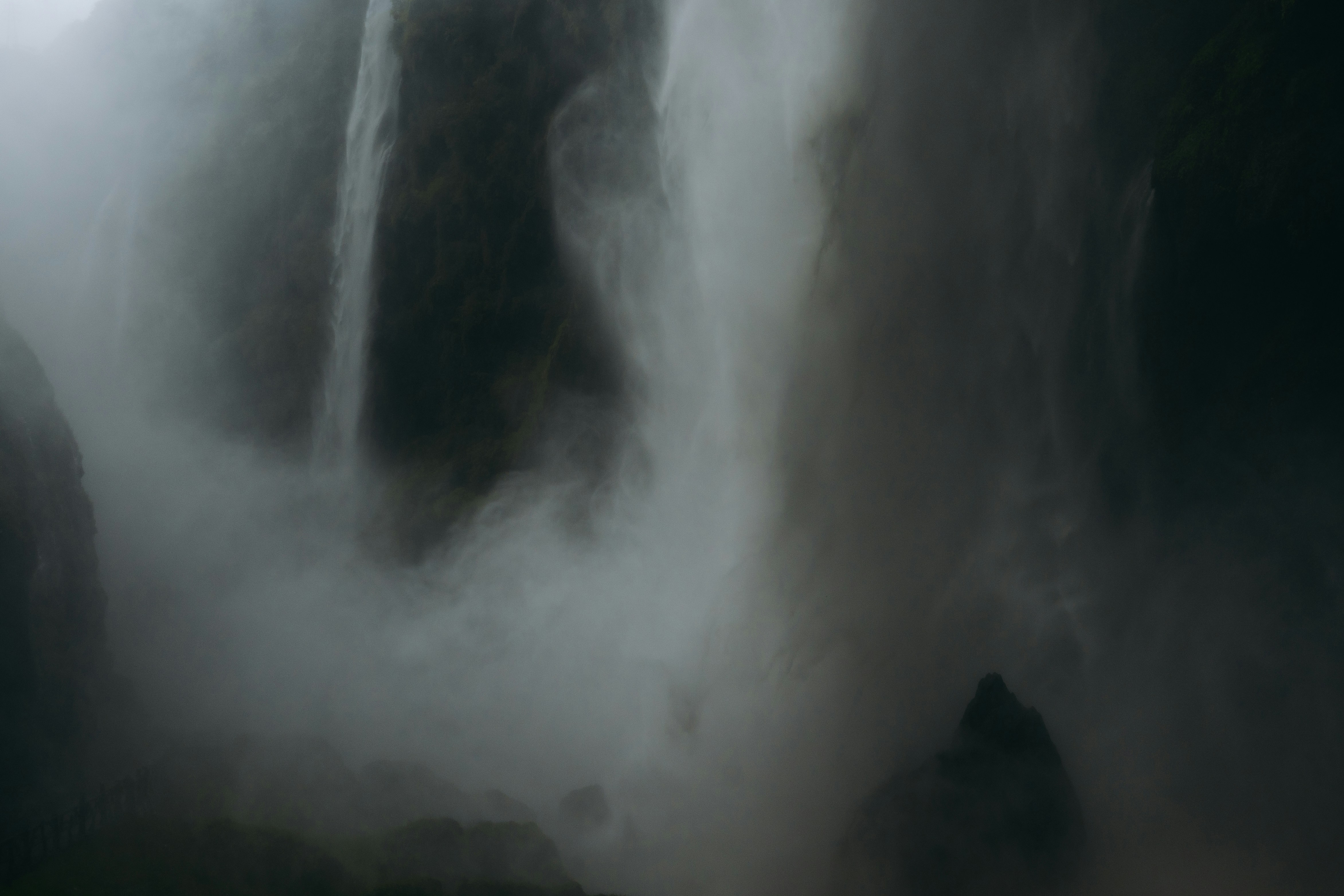 Waterfall cascading into a misty, dimly lit canyon.