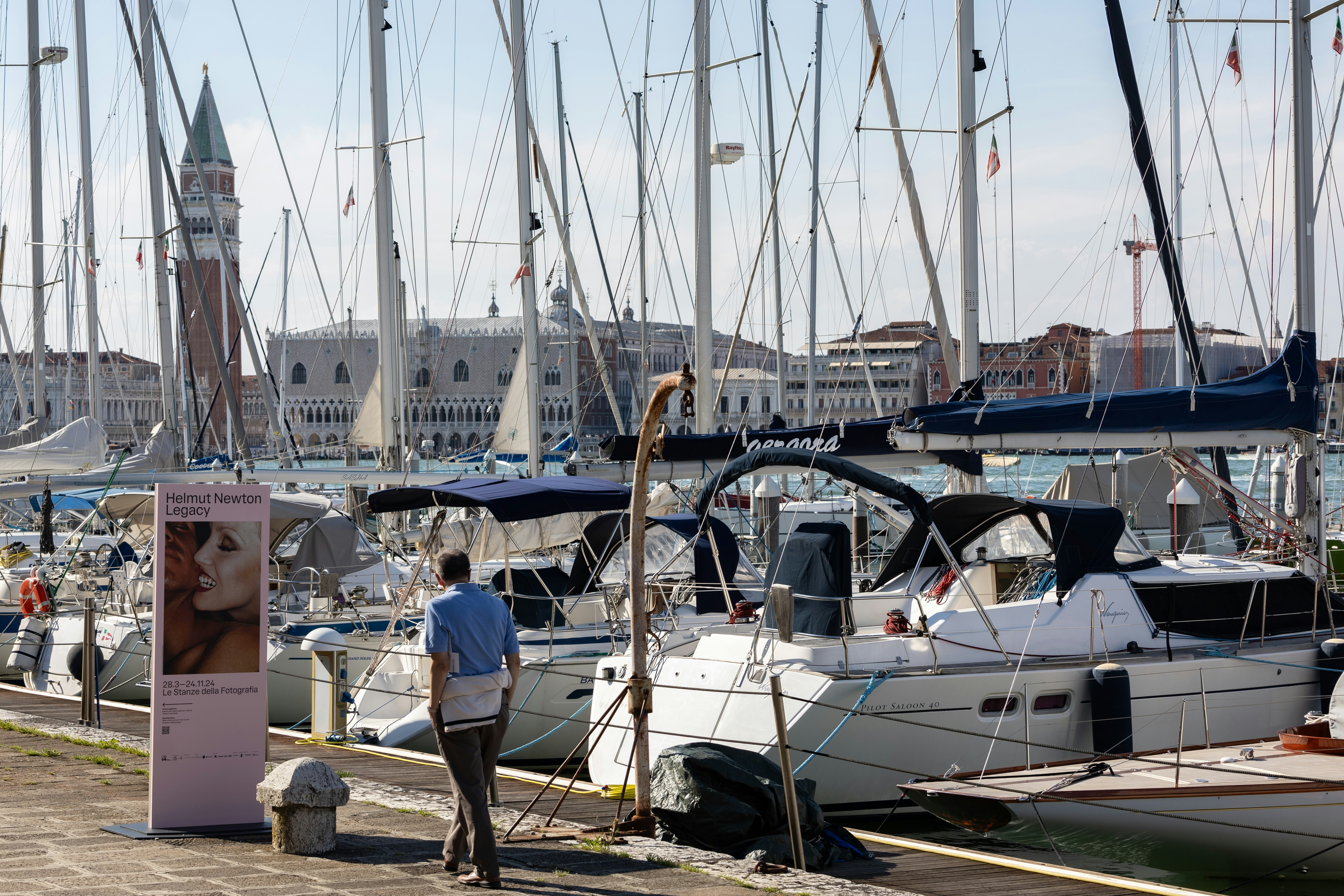 Man walking along a dock lined with yachts, with historic Venetian architecture in the background.