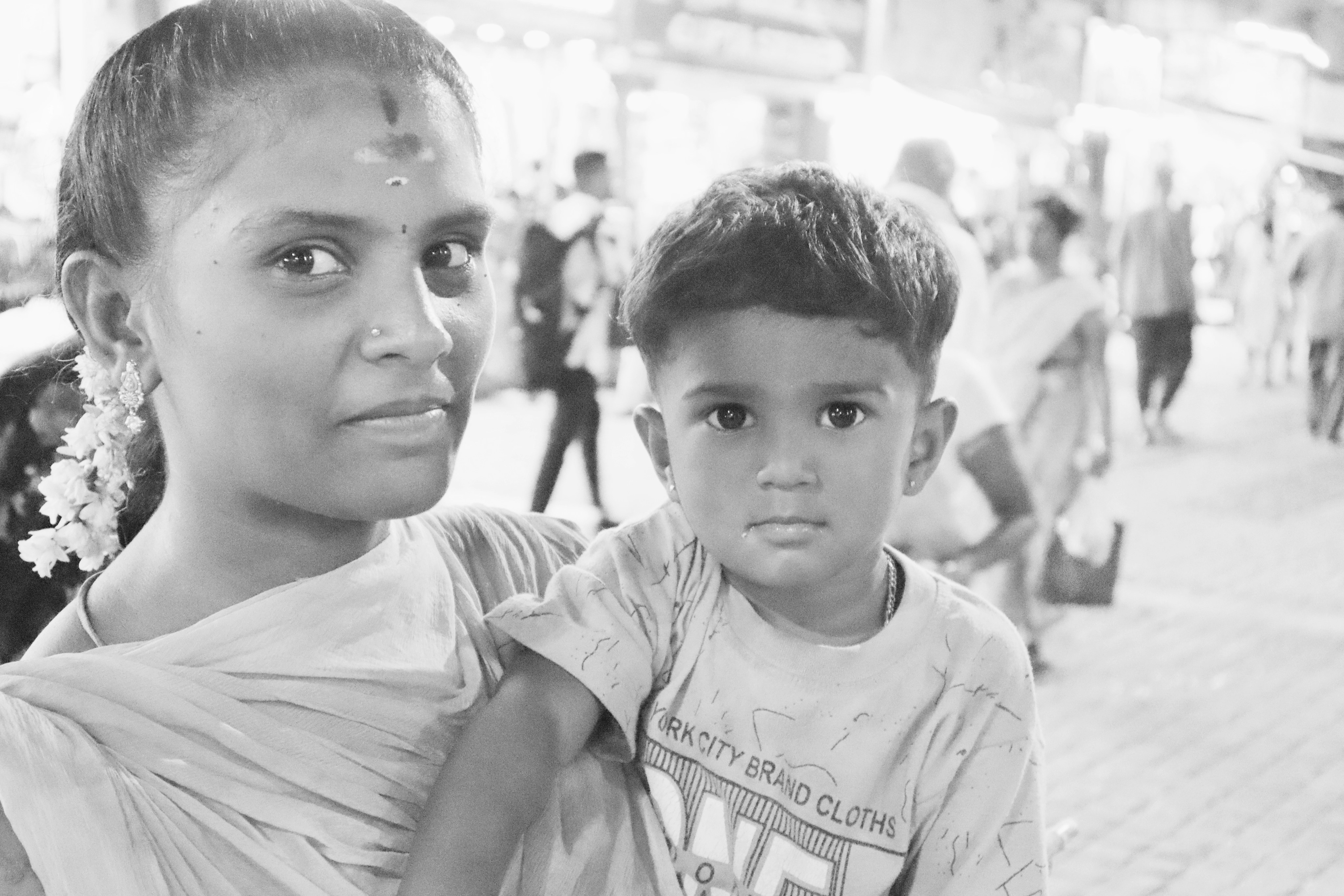 Black and white portrait of a woman holding a young boy in a busy street setting.
