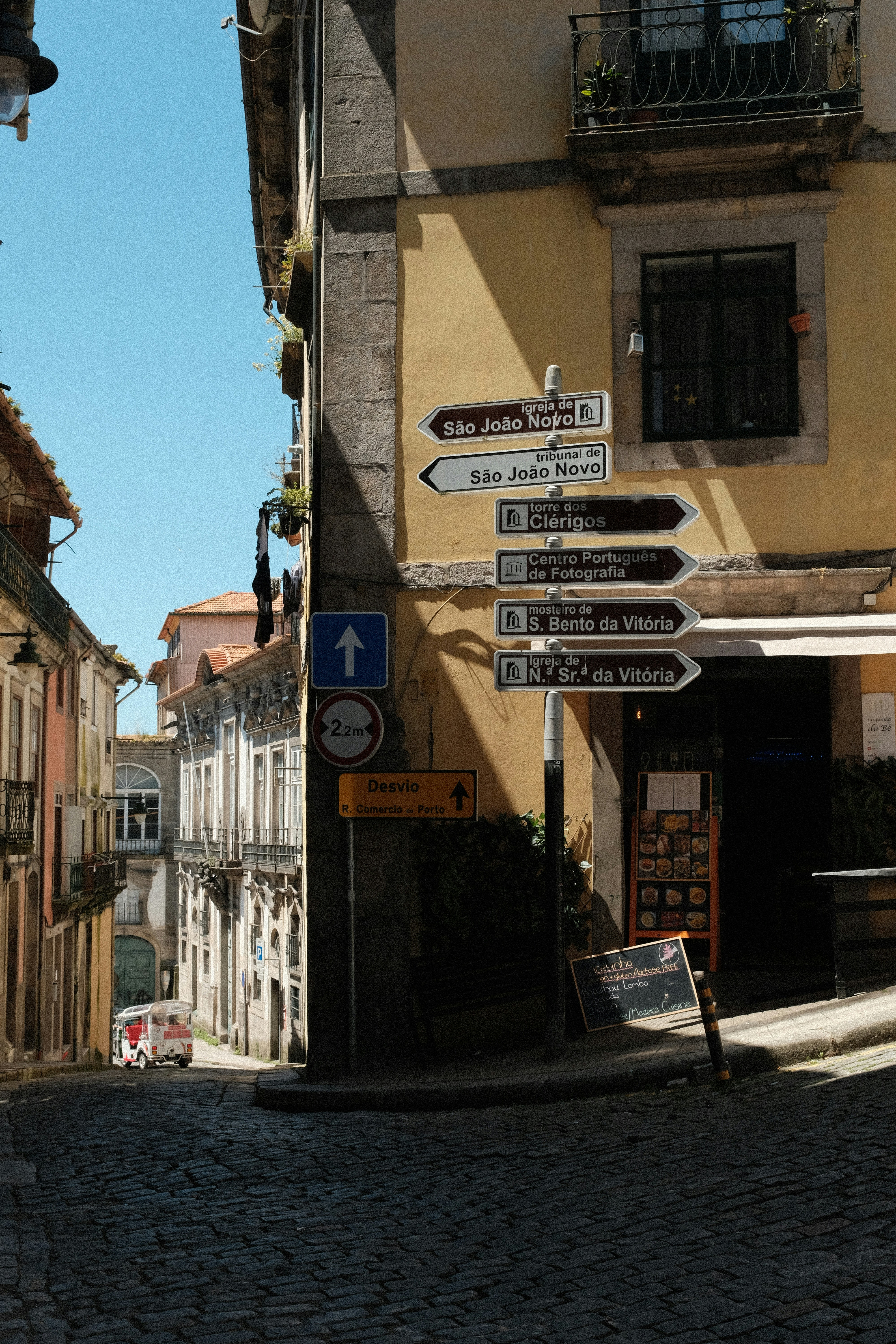 A quaint street in Porto featuring directional signs pointing to various landmarks, framed by historical architecture. The scene captures the essence of urban exploration.