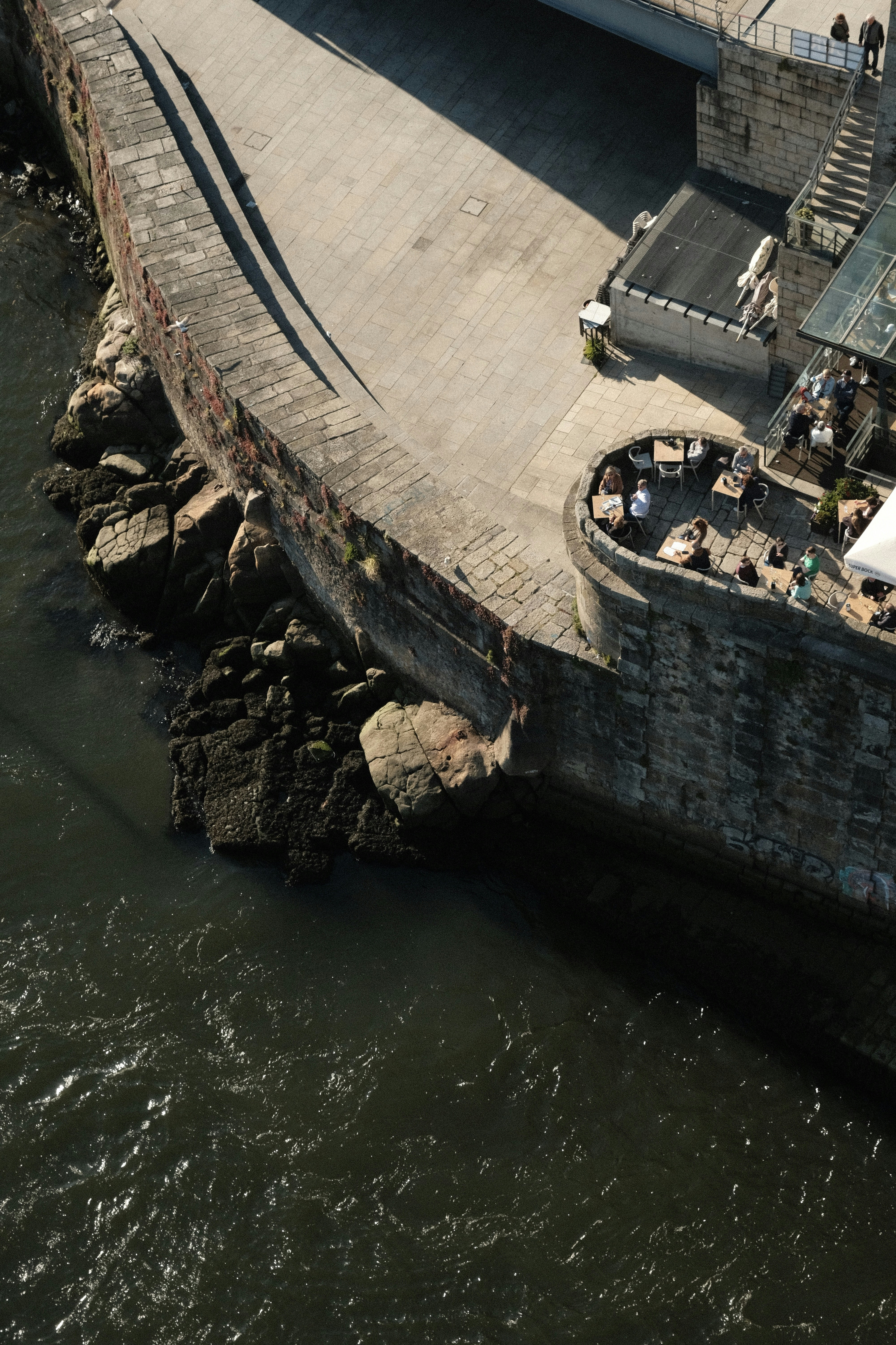 Sunlit Seawall Café: Afternoon Aerial over a Stone Terrace