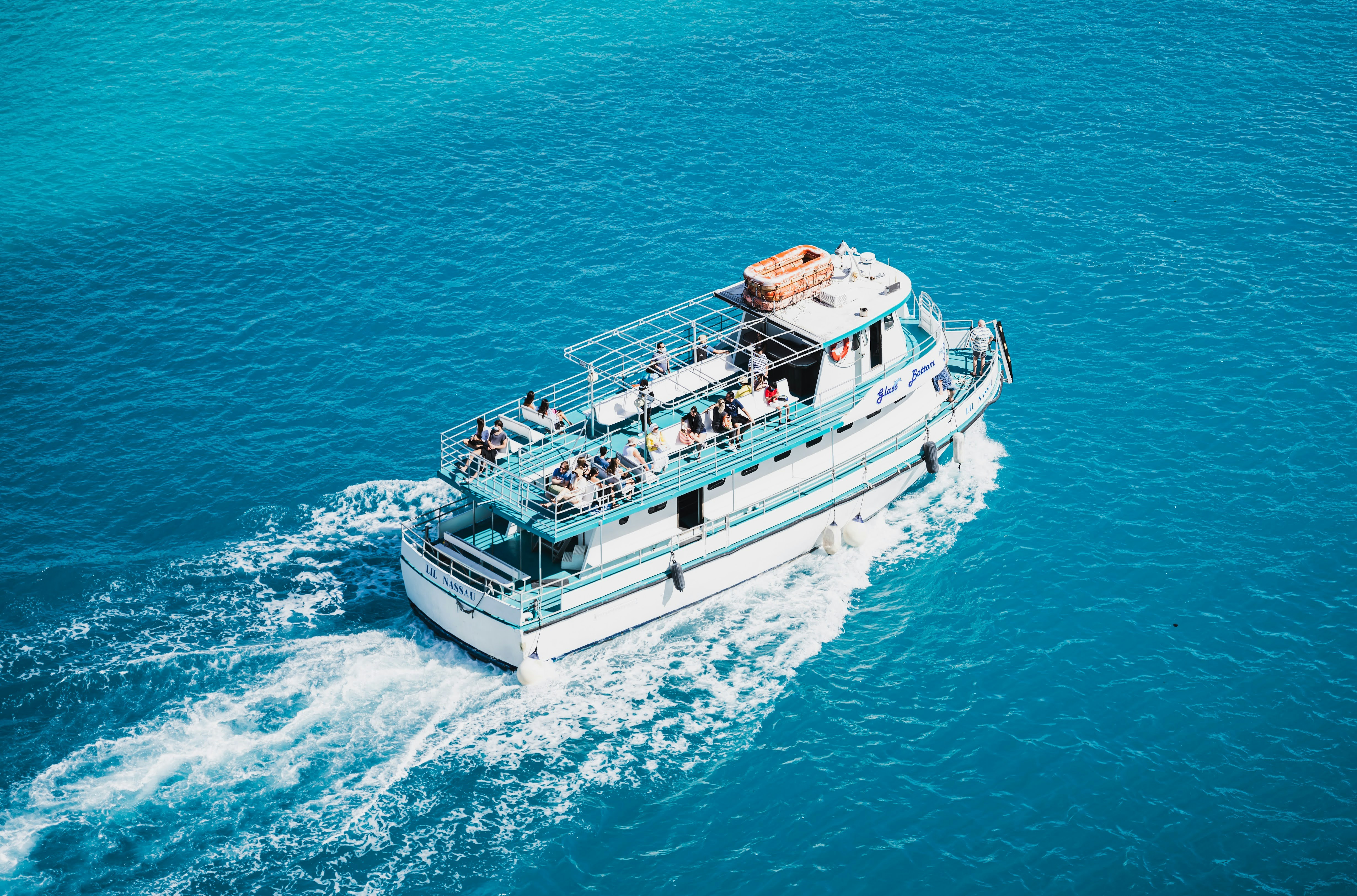 Tour boat gliding through vibrant turquoise waters, filled with passengers enjoying a sunny day at sea.