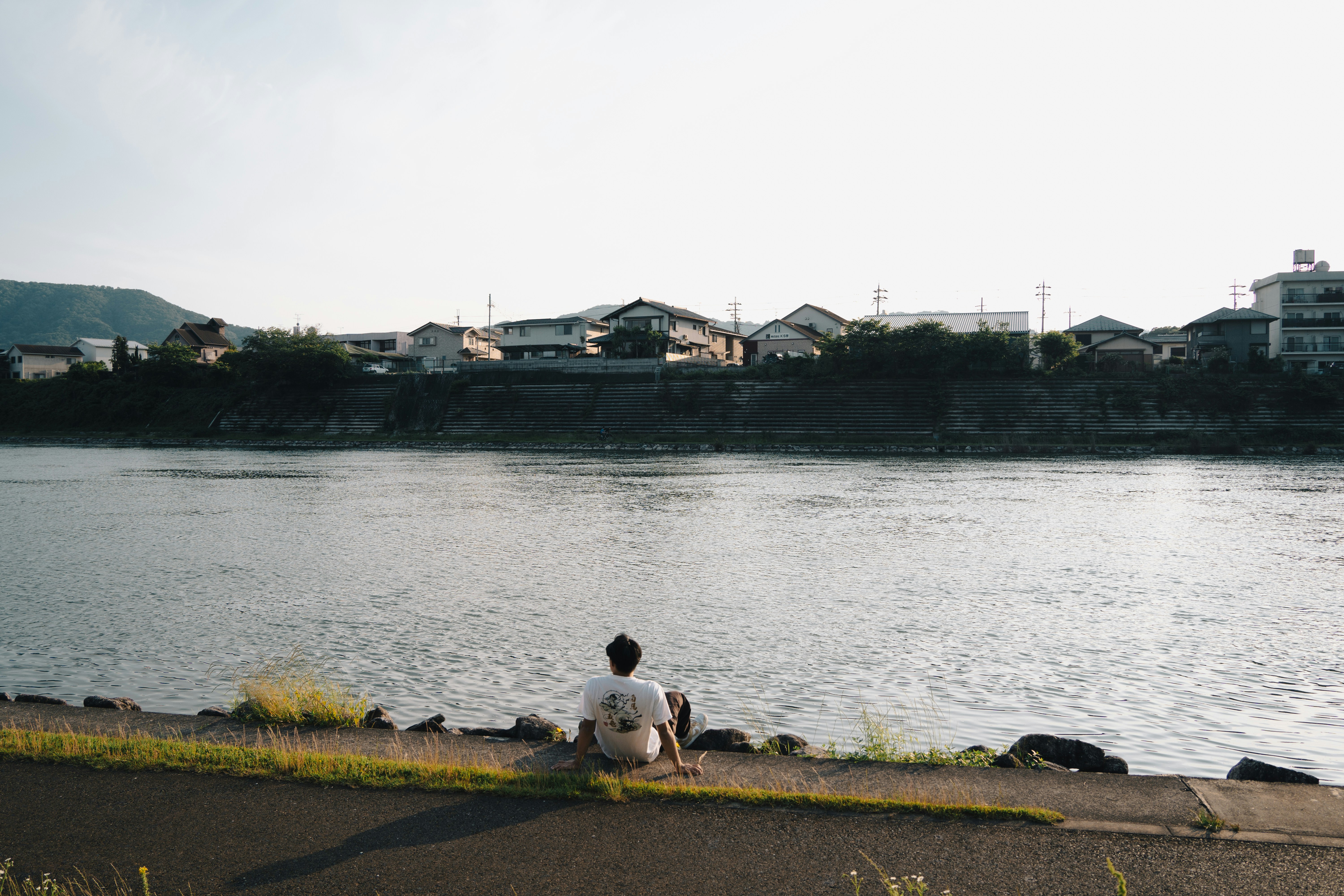 Bankside Quietude: A solitary figure gazes across the river toward a distant town