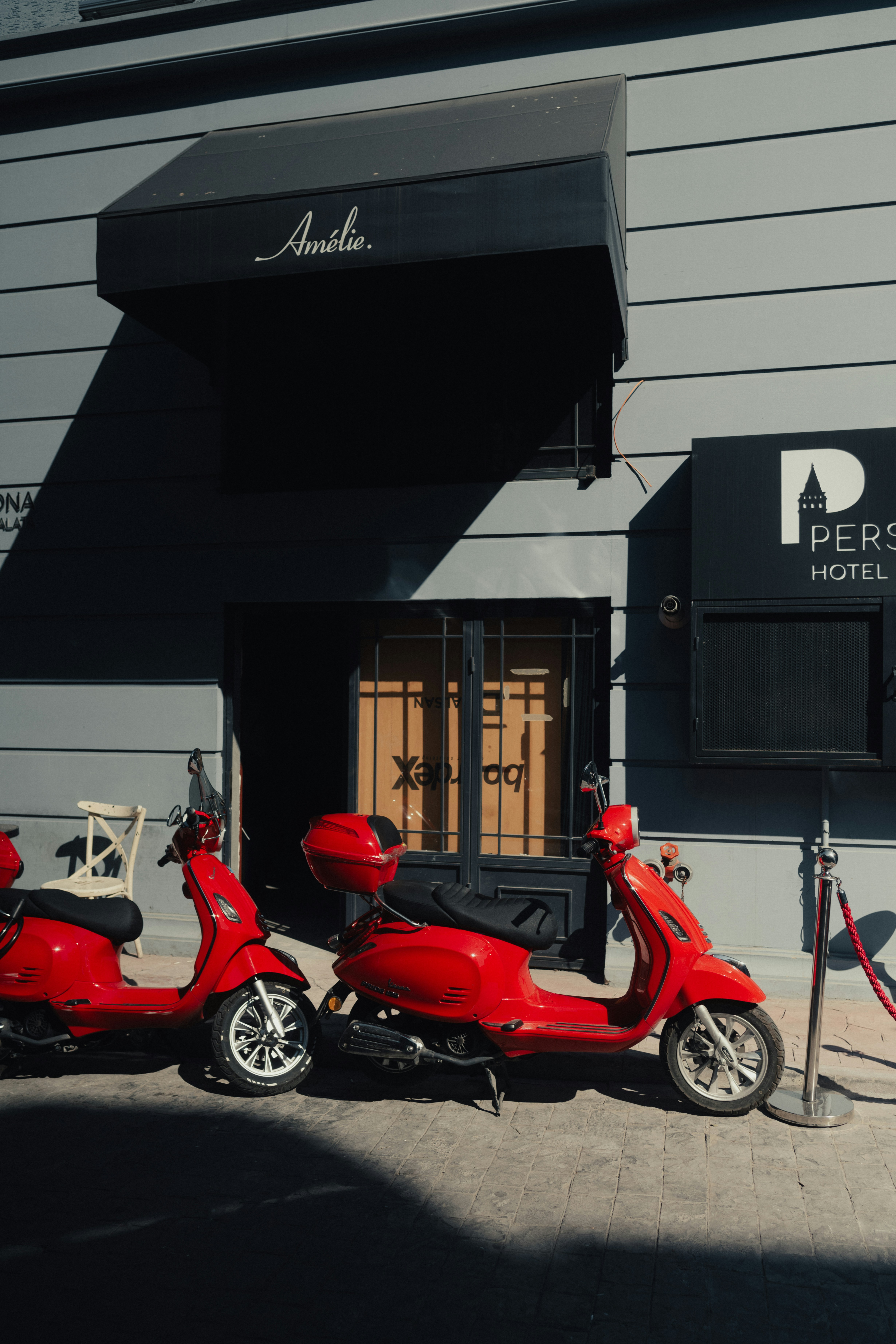Red Vespas by a shadowed storefront under Amélie awning