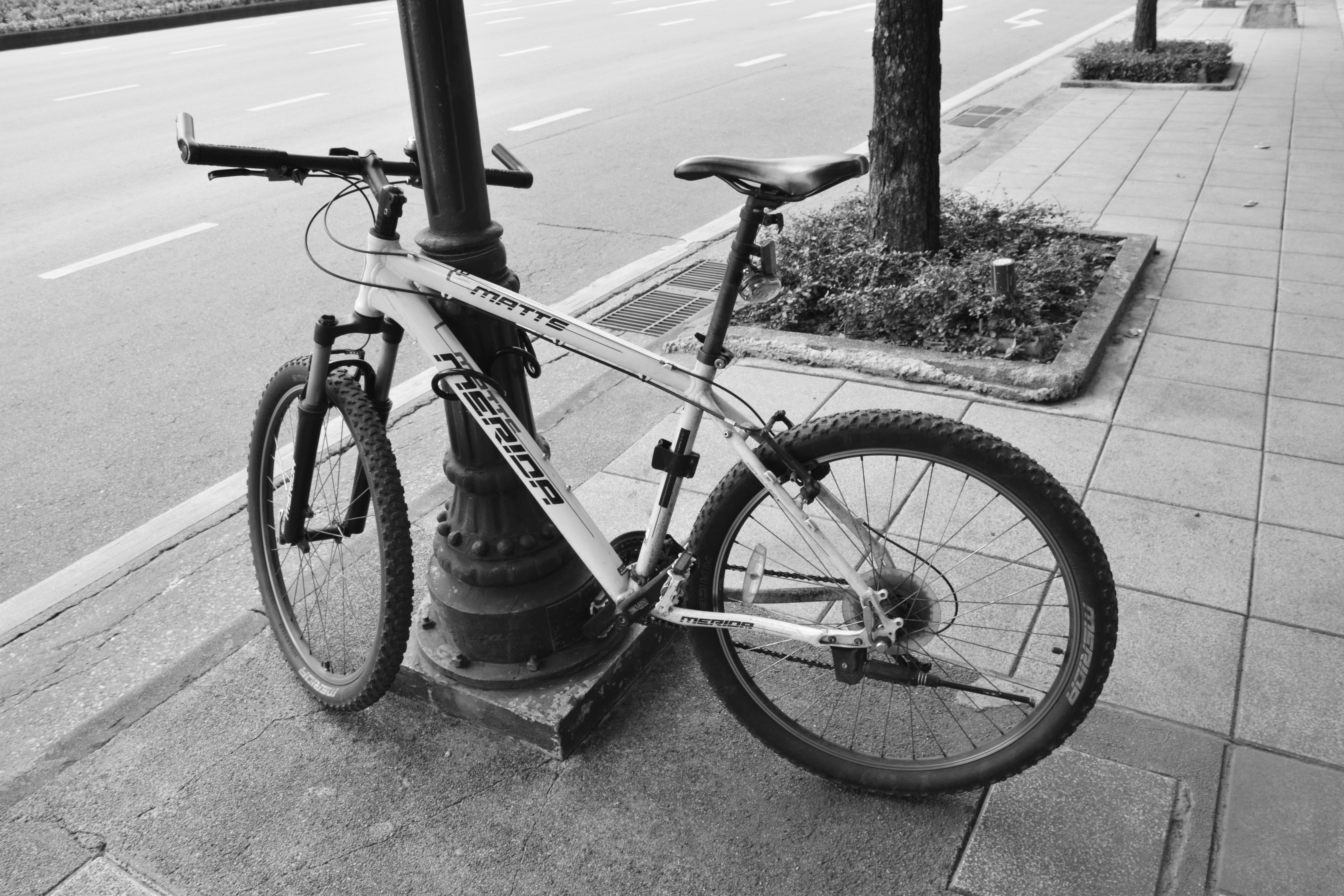 A bicycle is chained to a pole on the sidewalk photo – Free Thailand ...