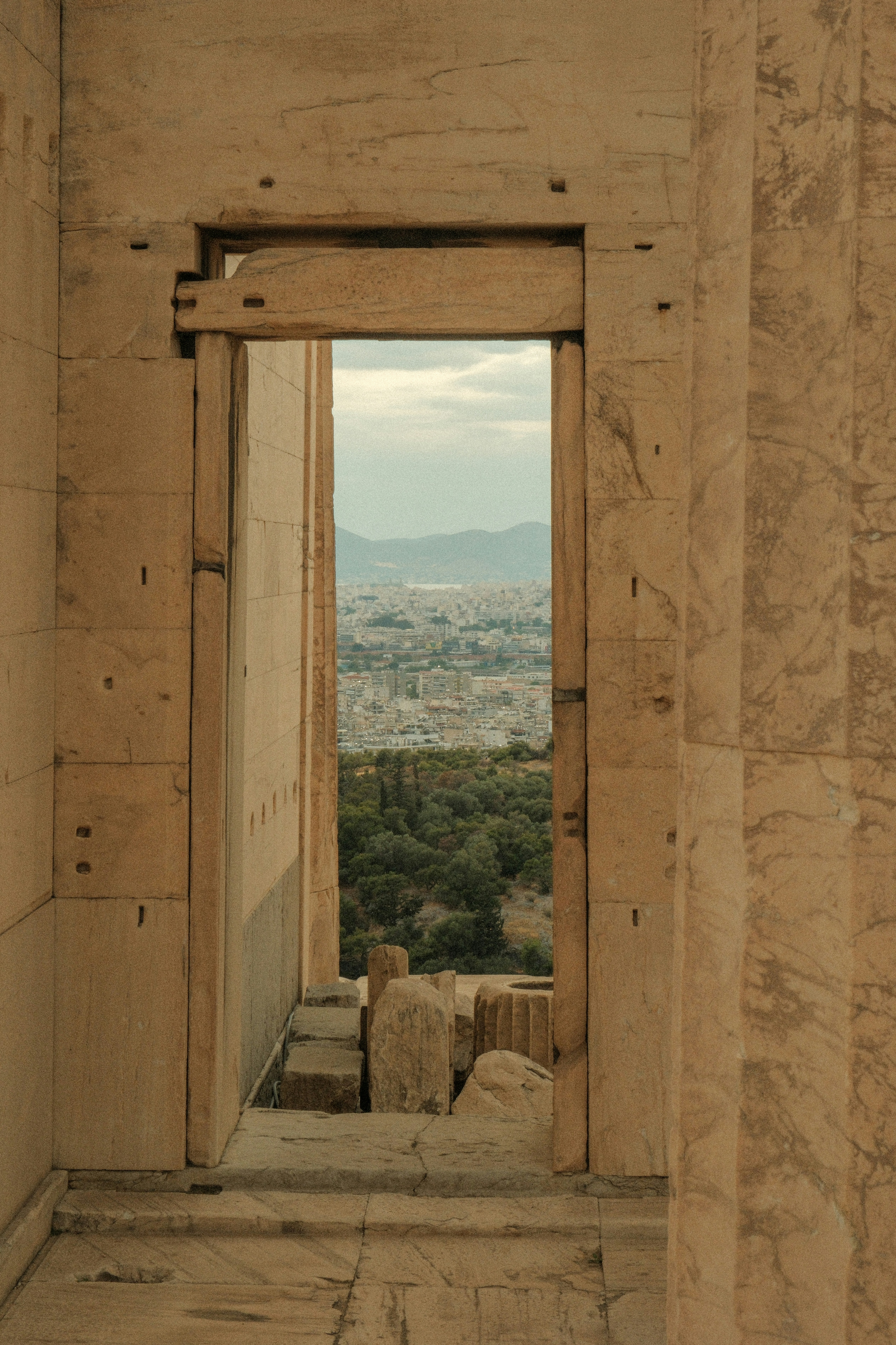 Marble corridor frames a distant cityscape through a narrow doorway, with weathered steps inviting viewers toward the panorama.