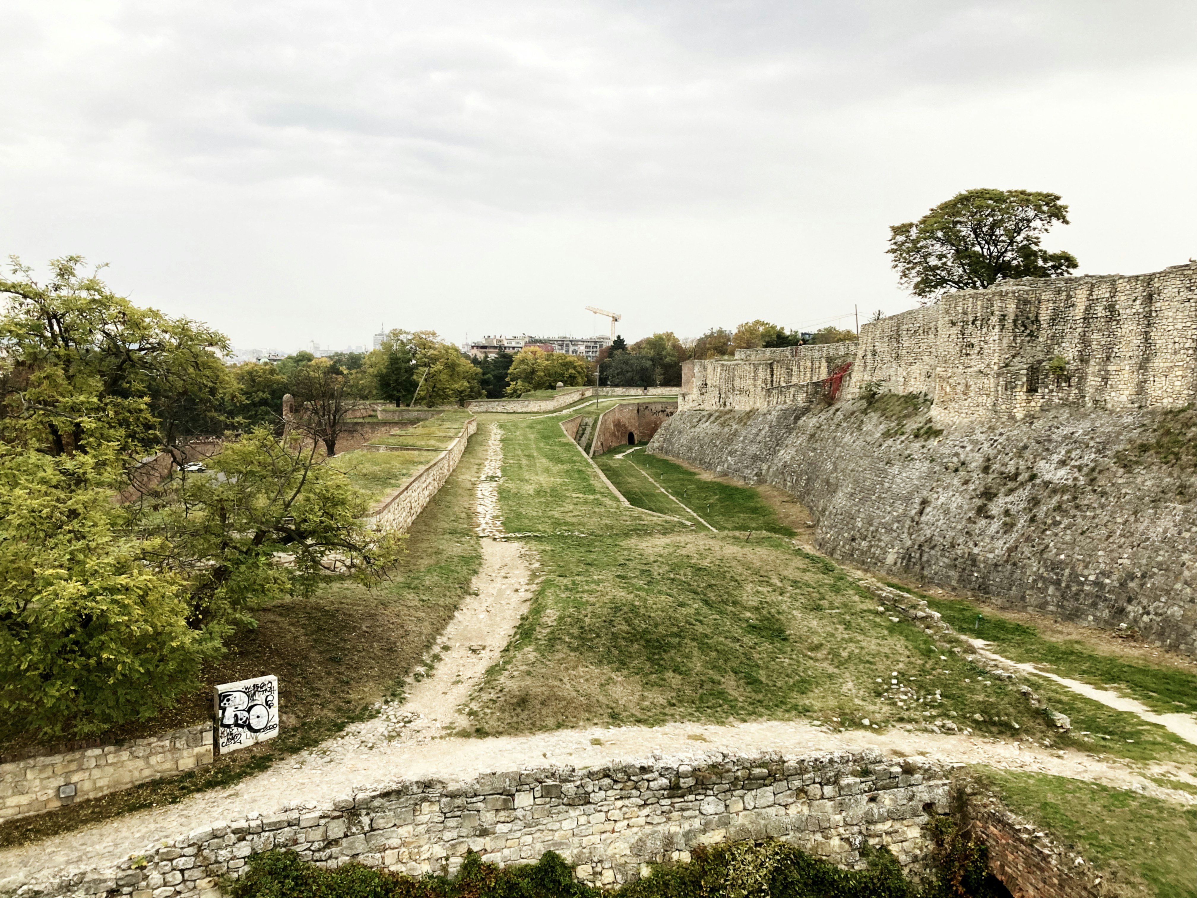 Stone wall with grassy path leading through a historic fortification under a cloudy sky.
