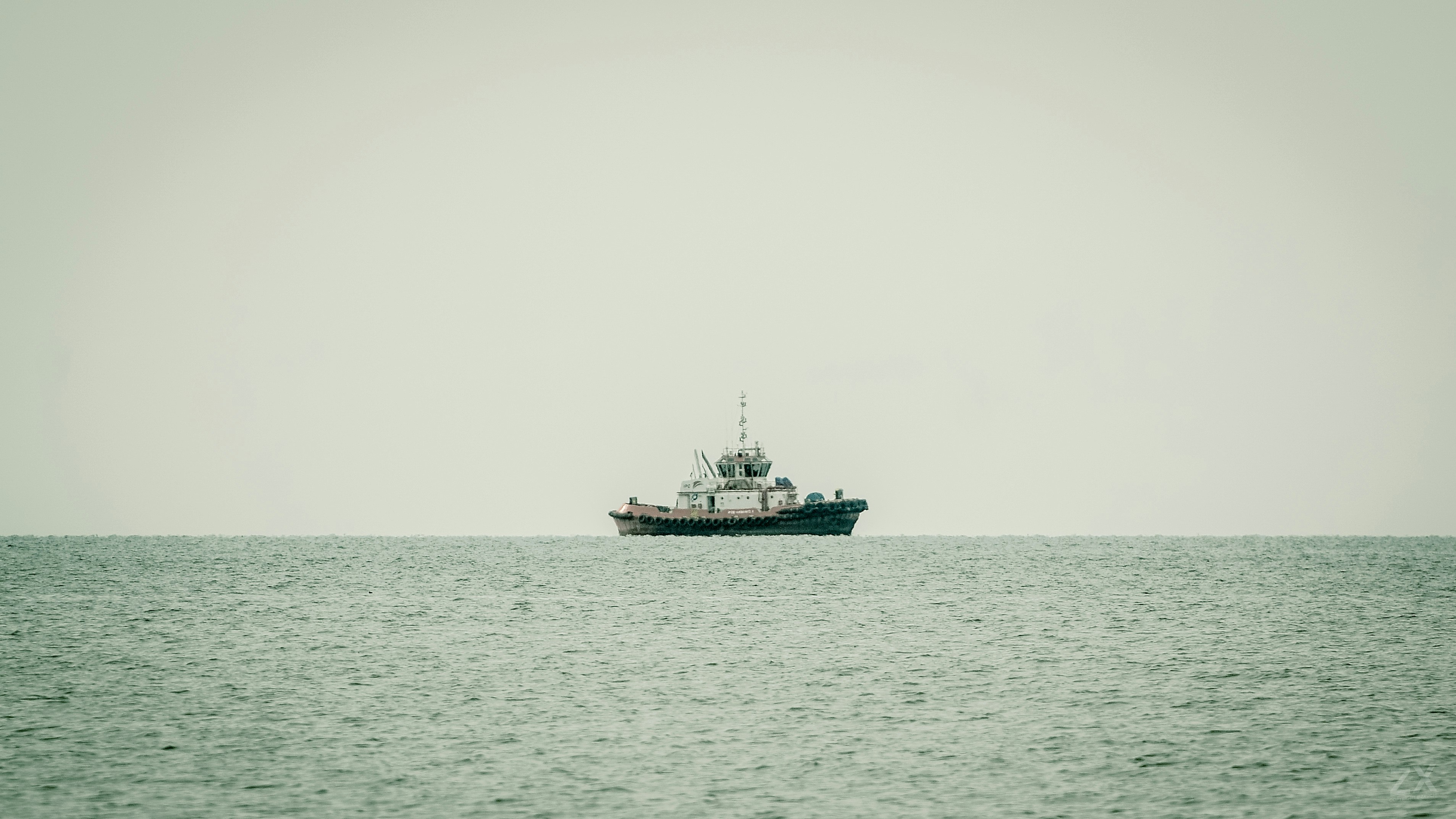 Boat sailing alone on a calm sea under a pale sky.