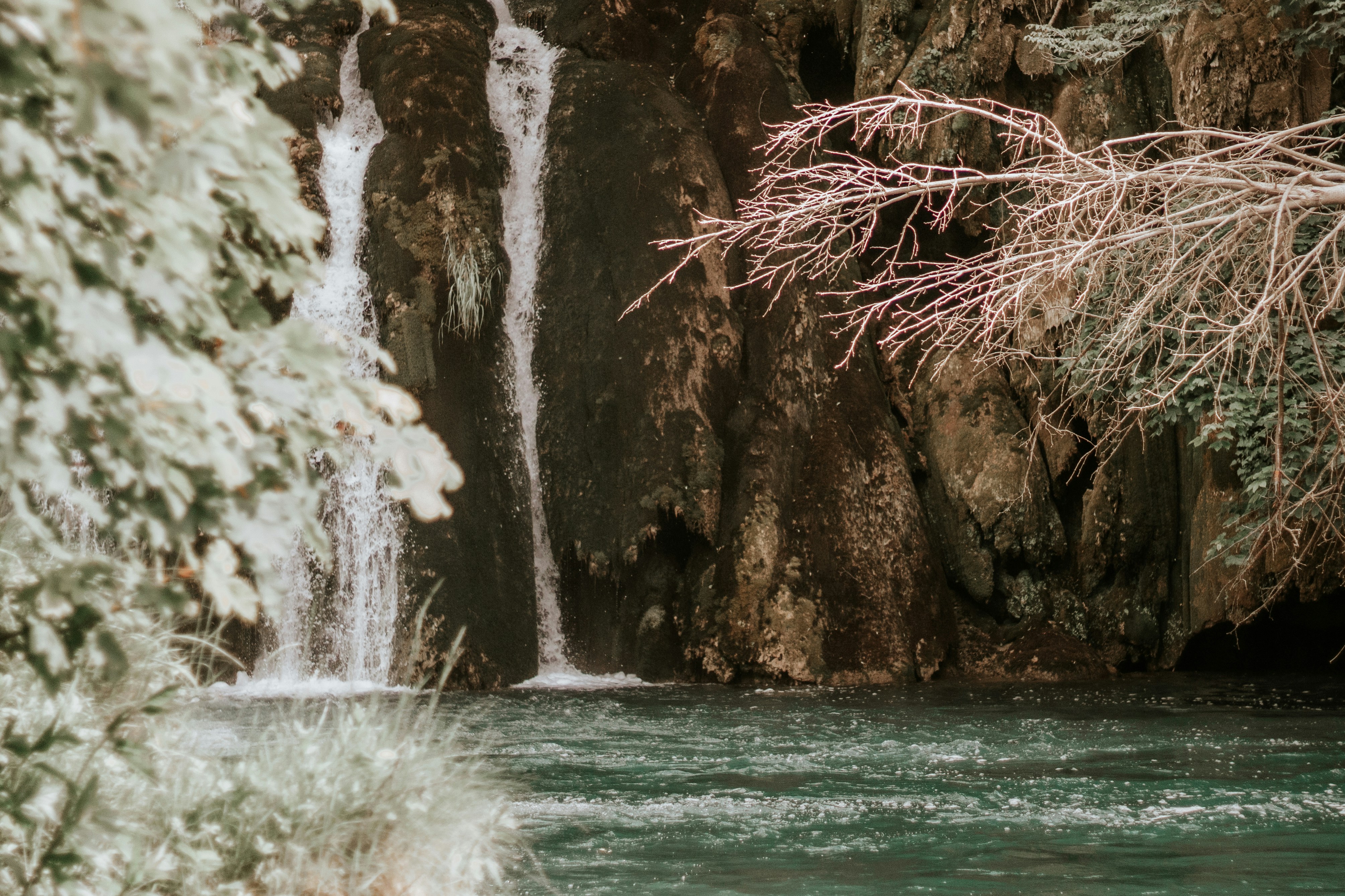 Two slender waterfalls cascade into a serene, emerald pool surrounded by lush greenery and rocky cliffs.