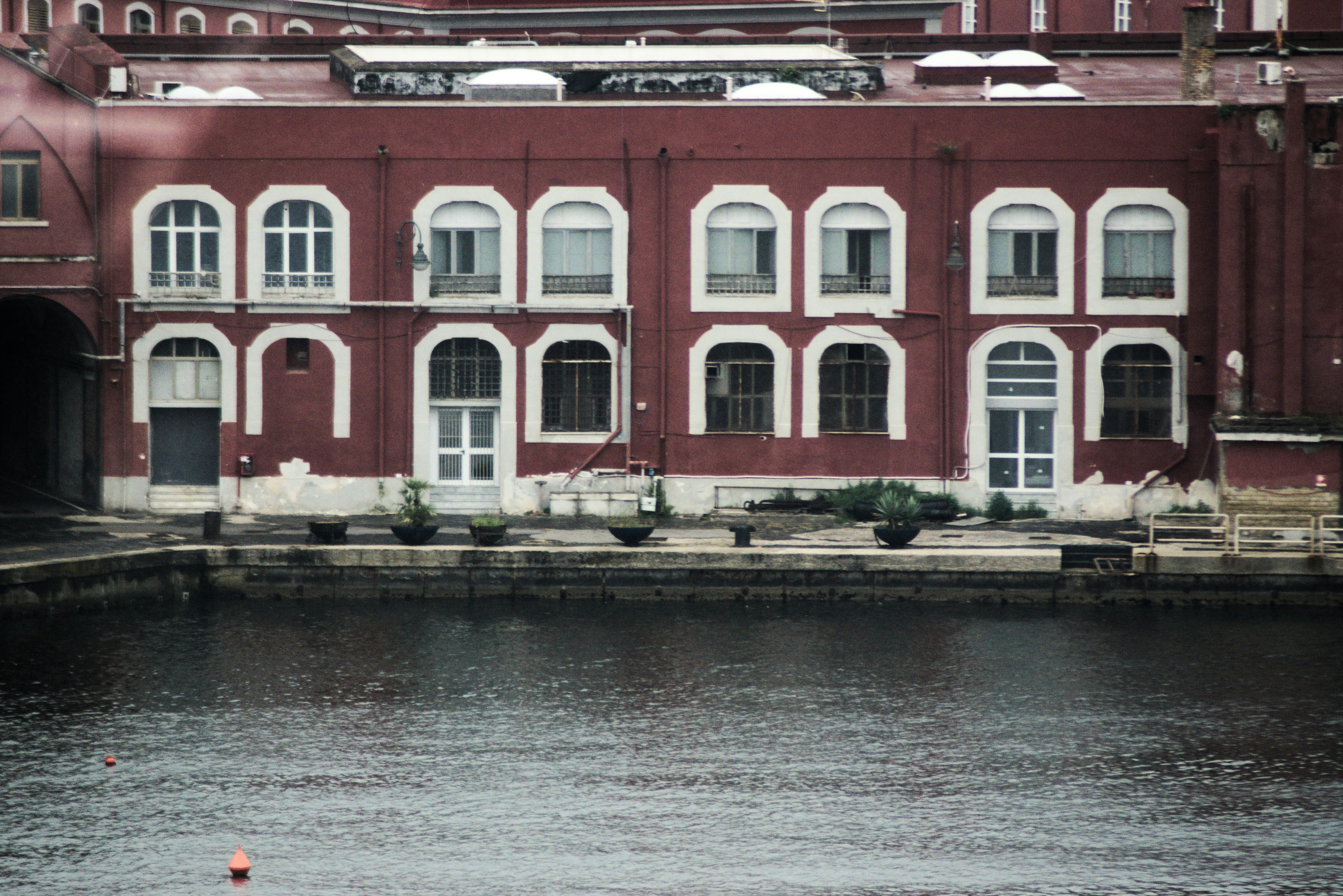 A large red building sitting next to a body of water photo – Free City ...